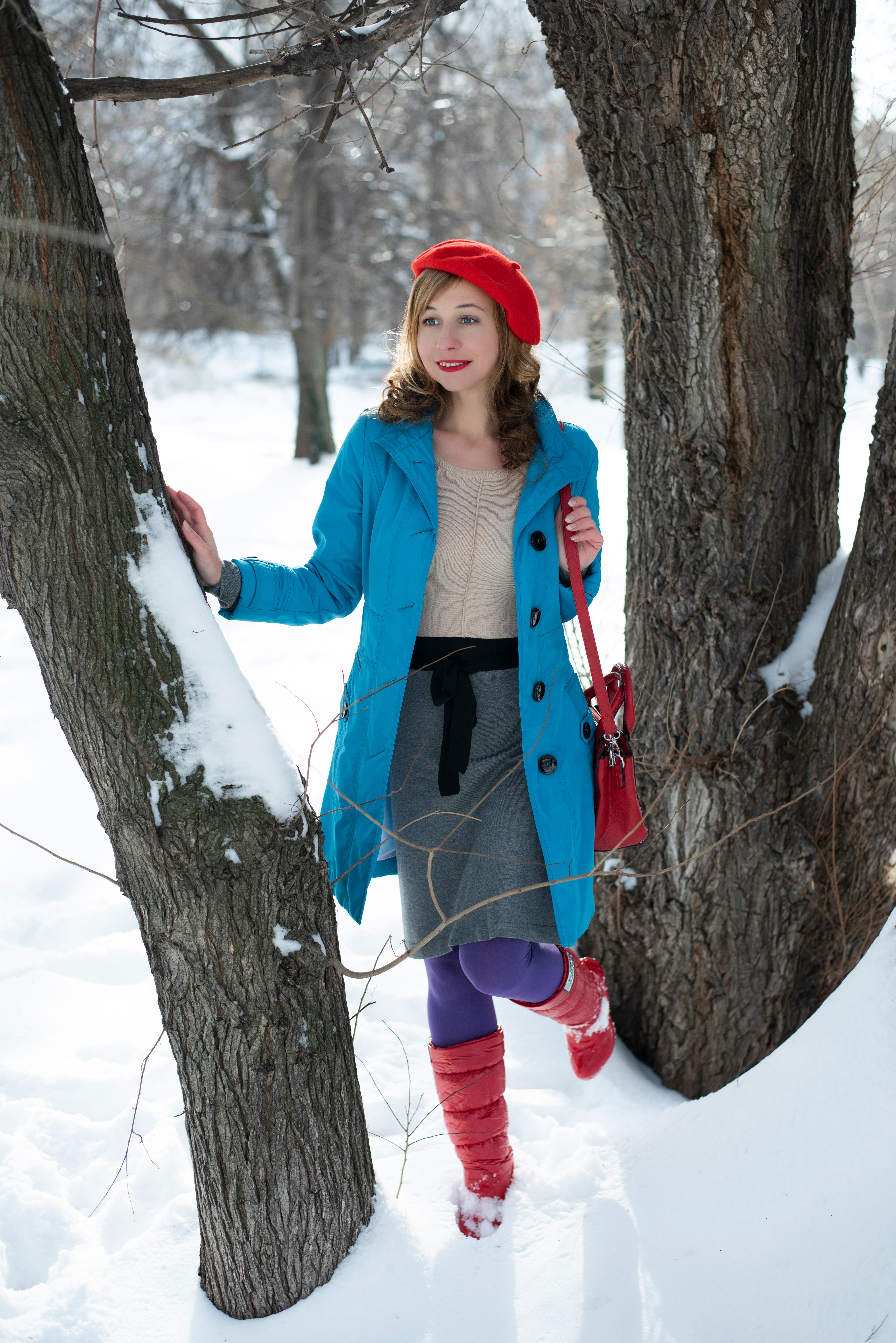A woman in red boots and a blue coat stands in the snow · Free Stock Photo