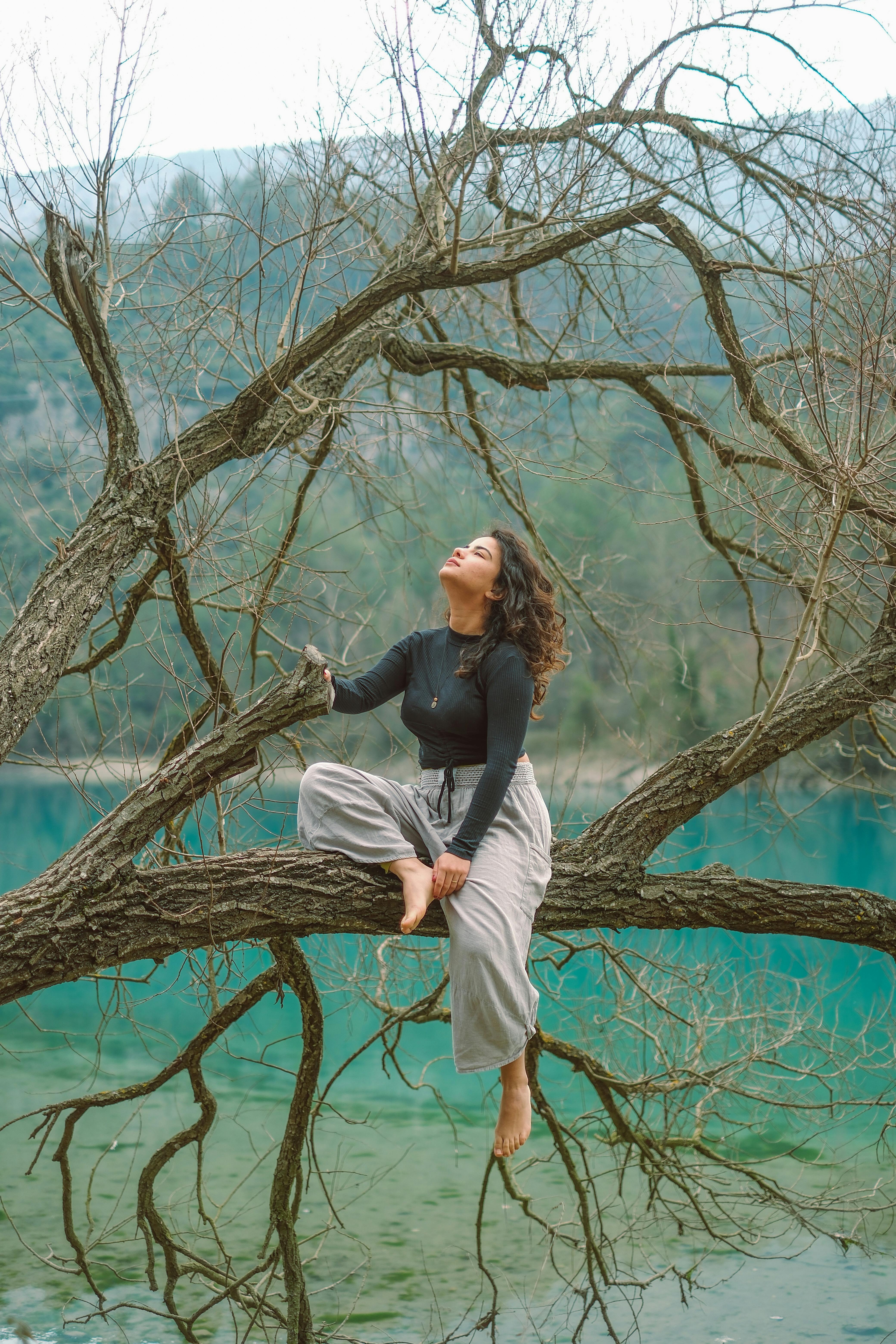 Woman Sitting on a Tree Branch by a Body of Water · Free Stock Photo