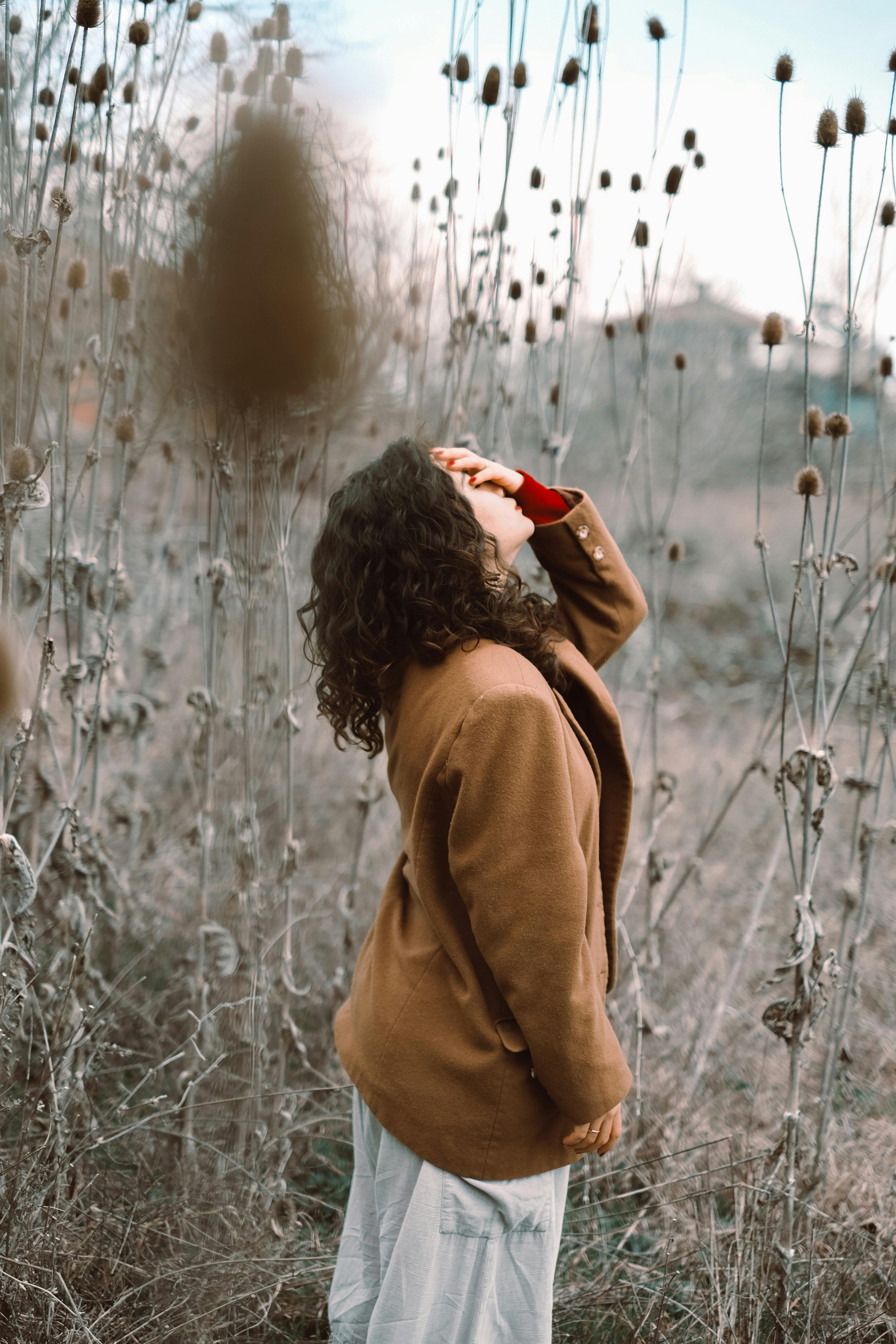 Woman in a Brown Coat with Hand on Her Face Standing Among the Shrubs ...