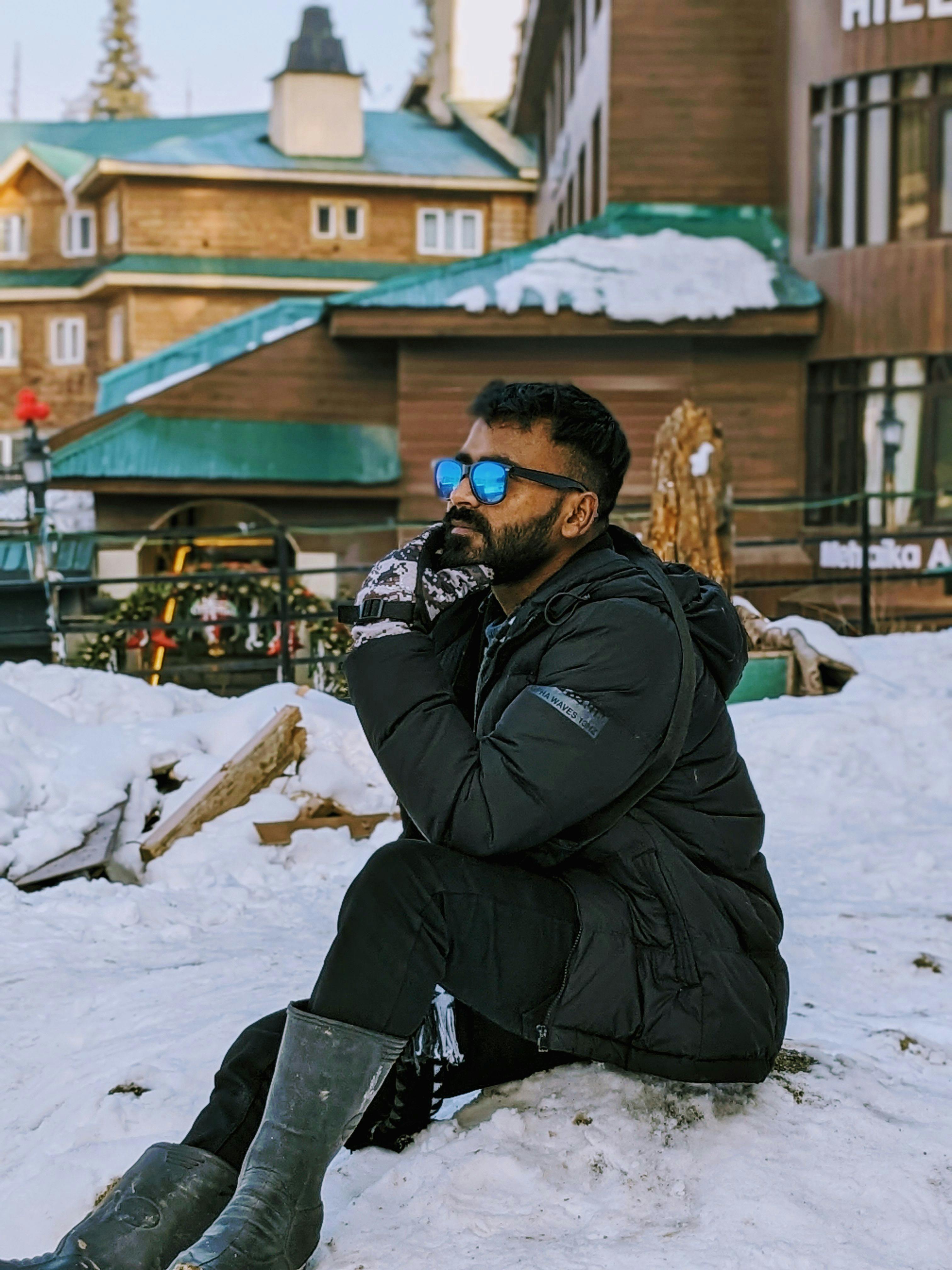 Man in Sunglasses and Black Jacket Sitting in Snow · Free Stock Photo