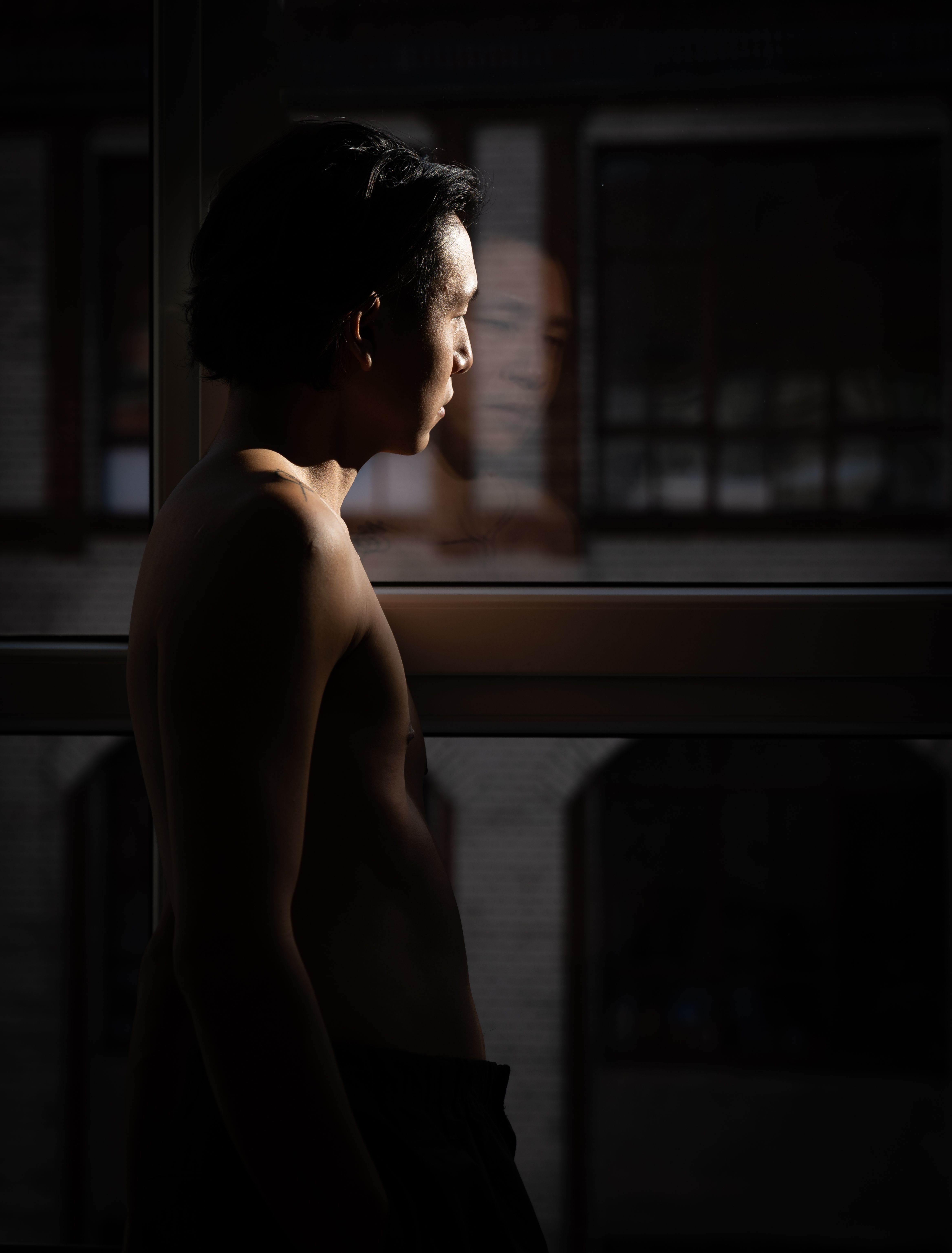 Side View of a Shirtless Man Standing next to a Window · Free Stock Photo