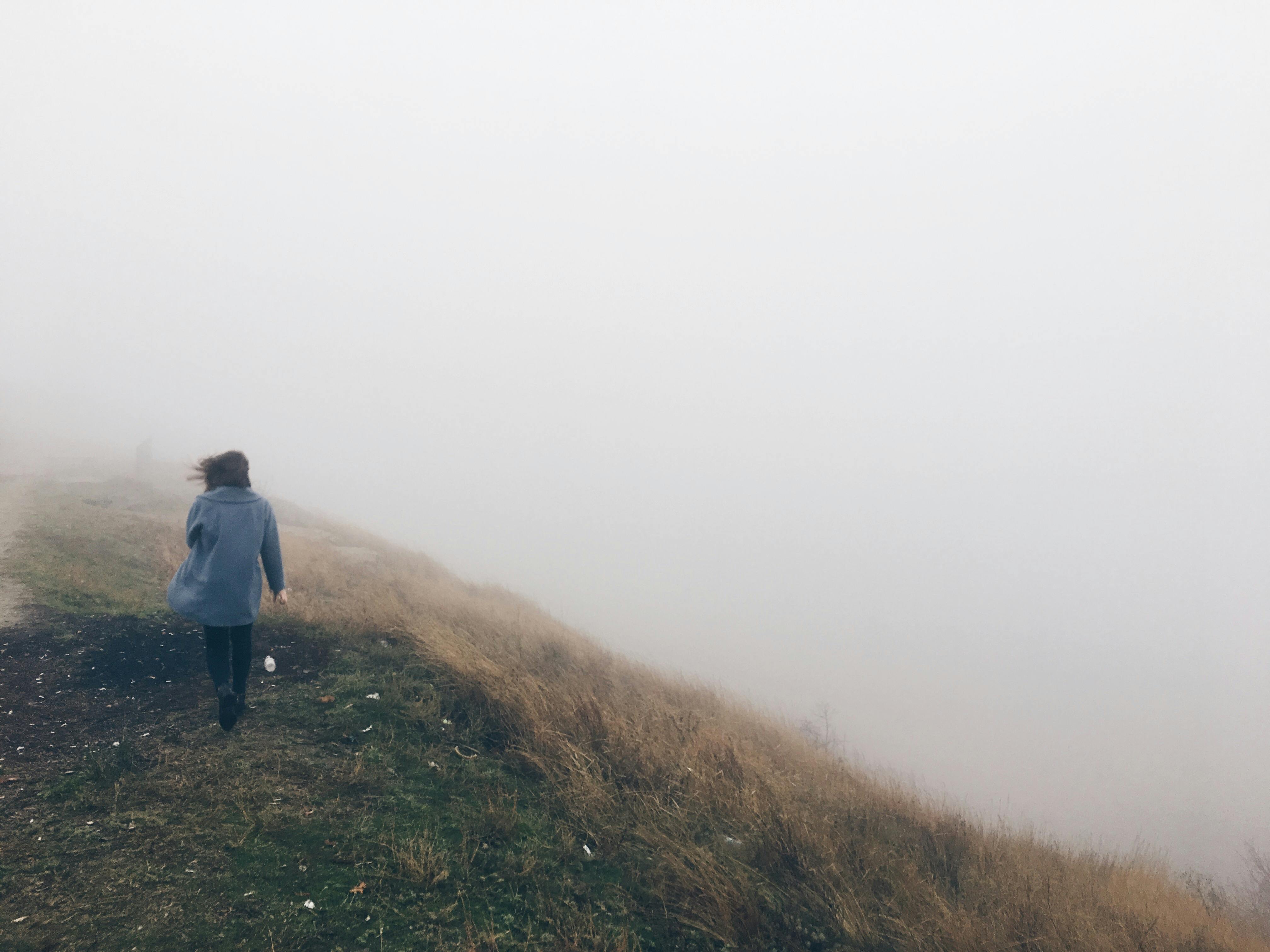 Back View of a Woman Walking Uphill in Dense Fog · Free Stock Photo