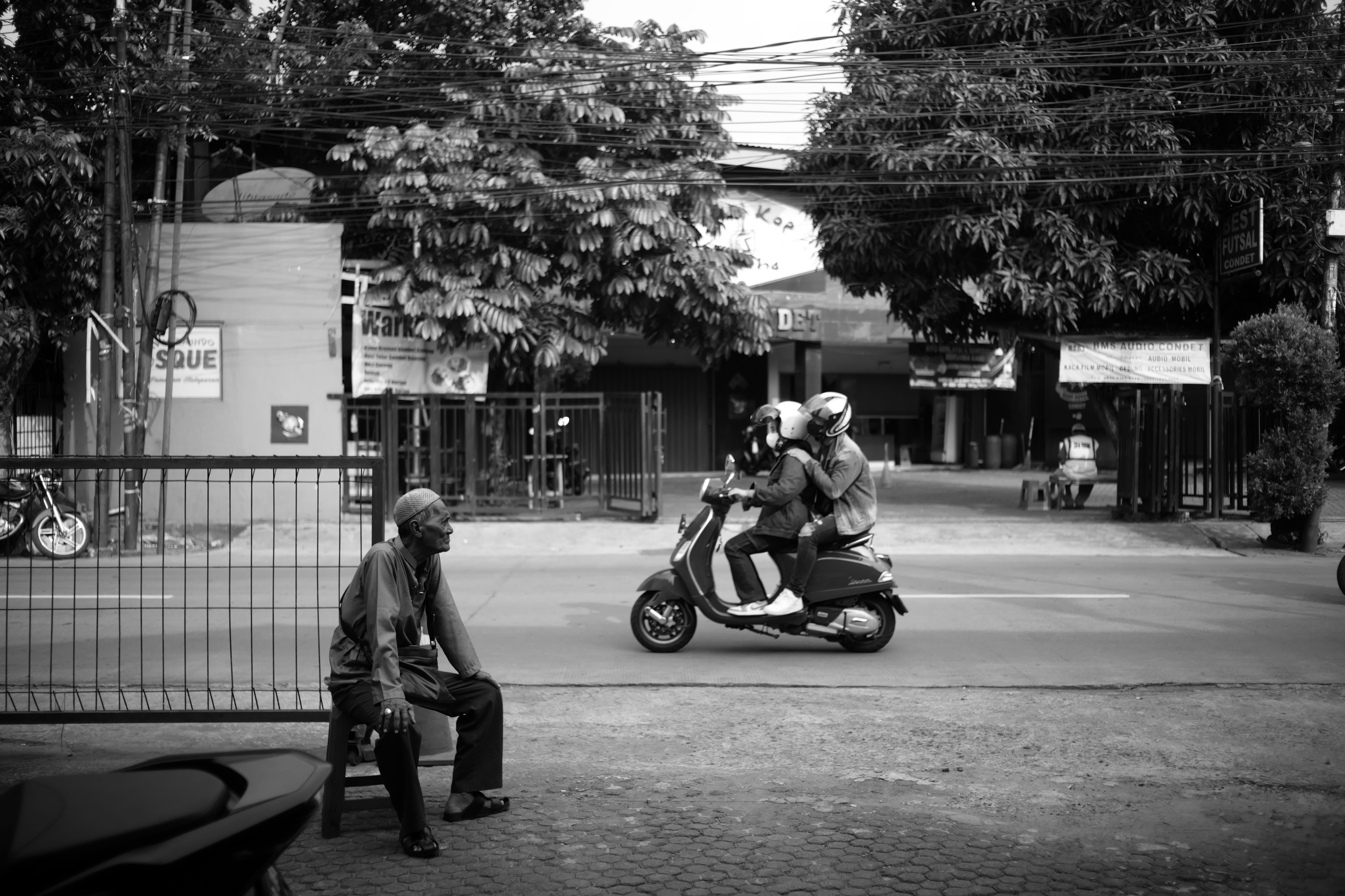 Couple Riding a Motor Scooter and an Elderly Man Sitting at the Gate of ...