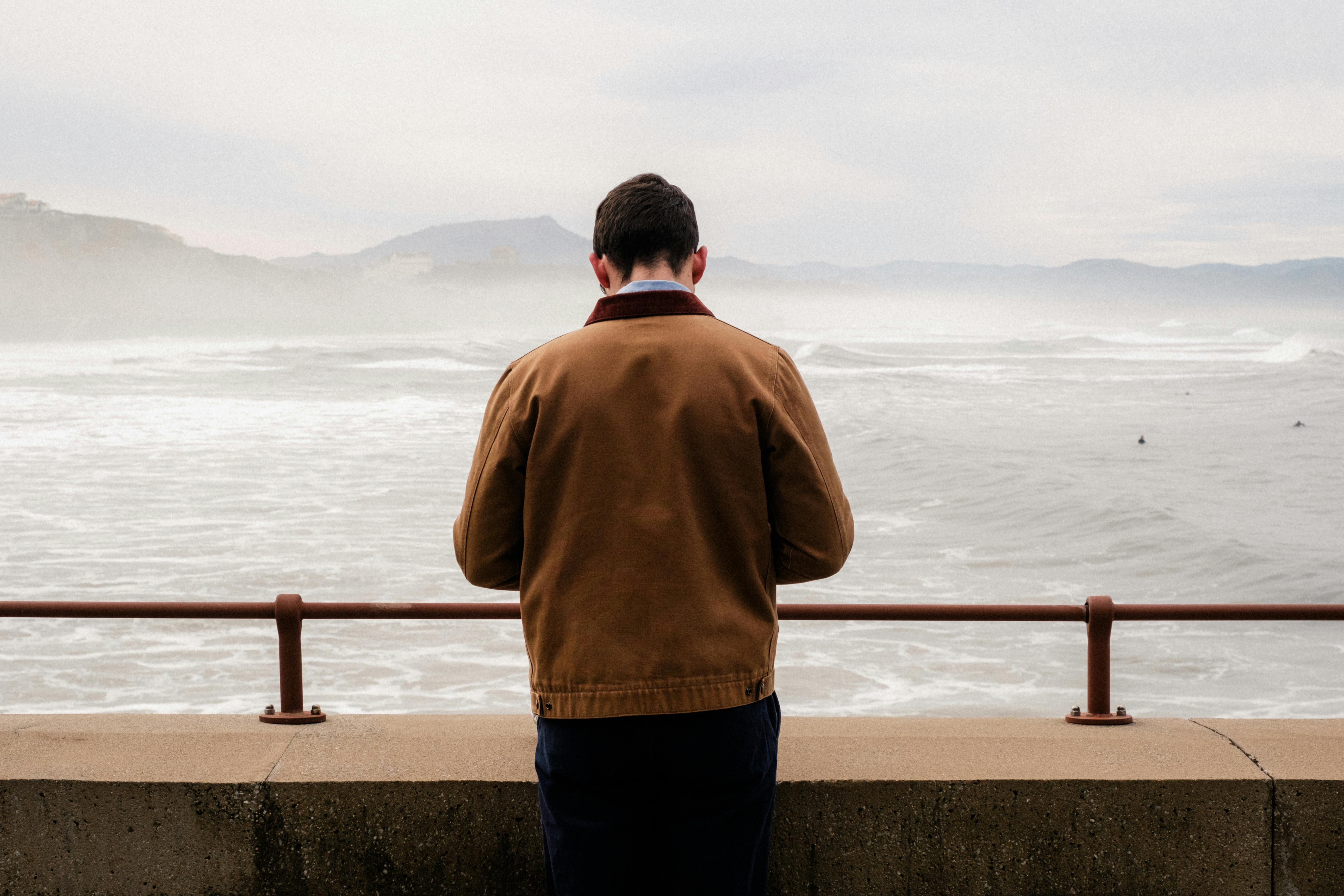 Back View of Man in Jacket Standing by Wall on Sea Shore · Free Stock Photo