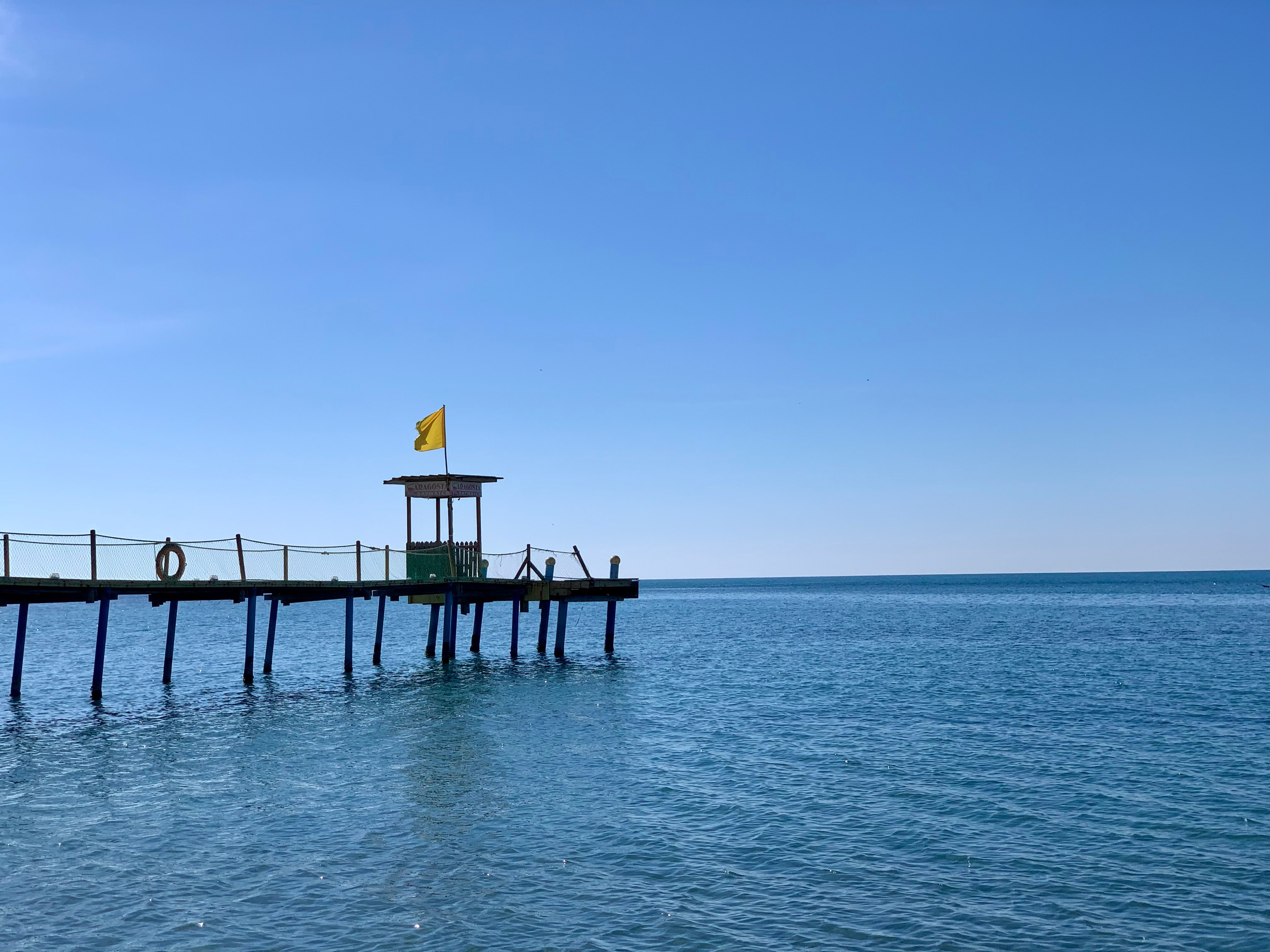 A pier with a yellow flag on it in the ocean · Free Stock Photo