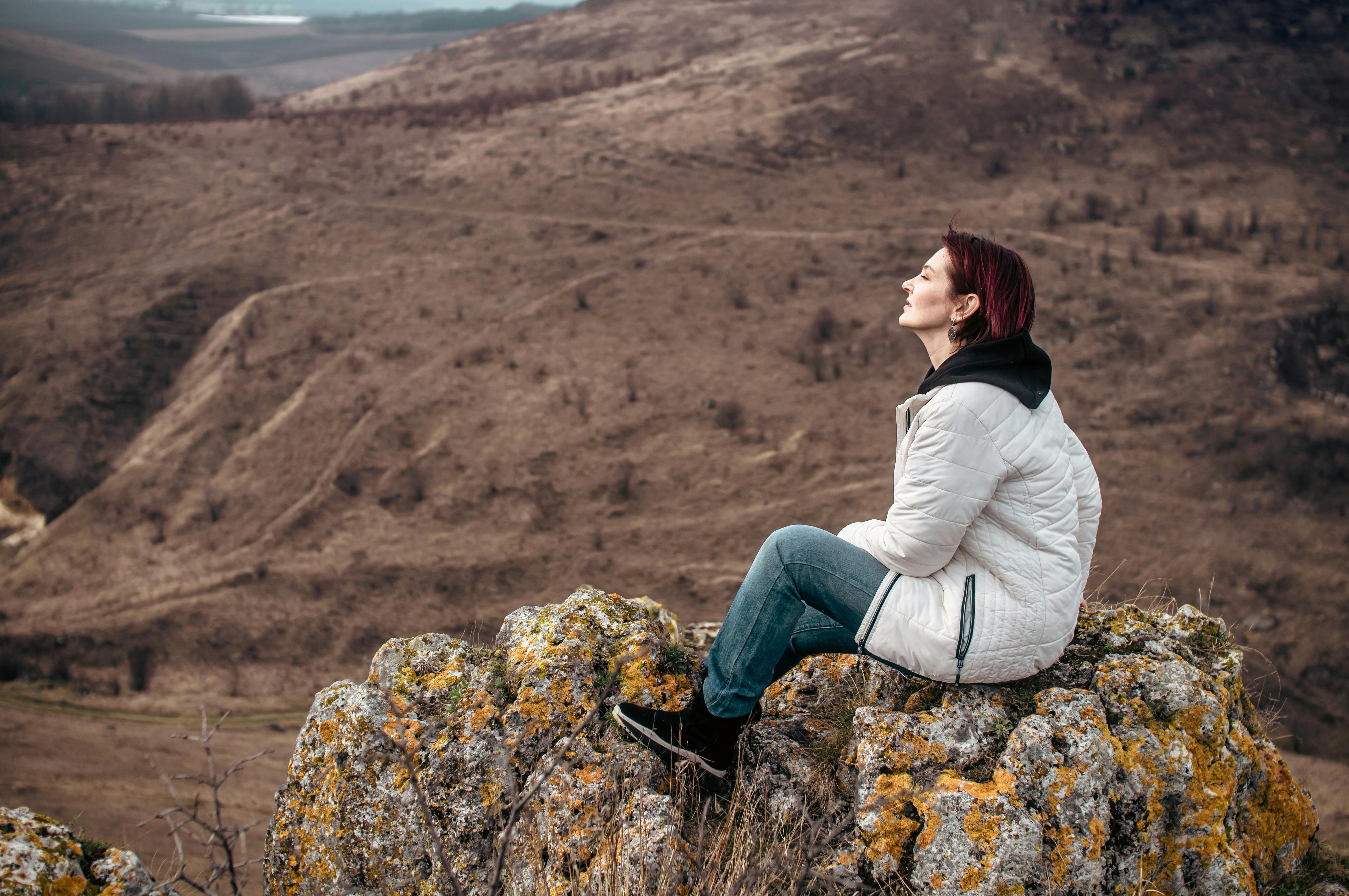 A woman sitting on a rock looking out over a valley · Free Stock Photo