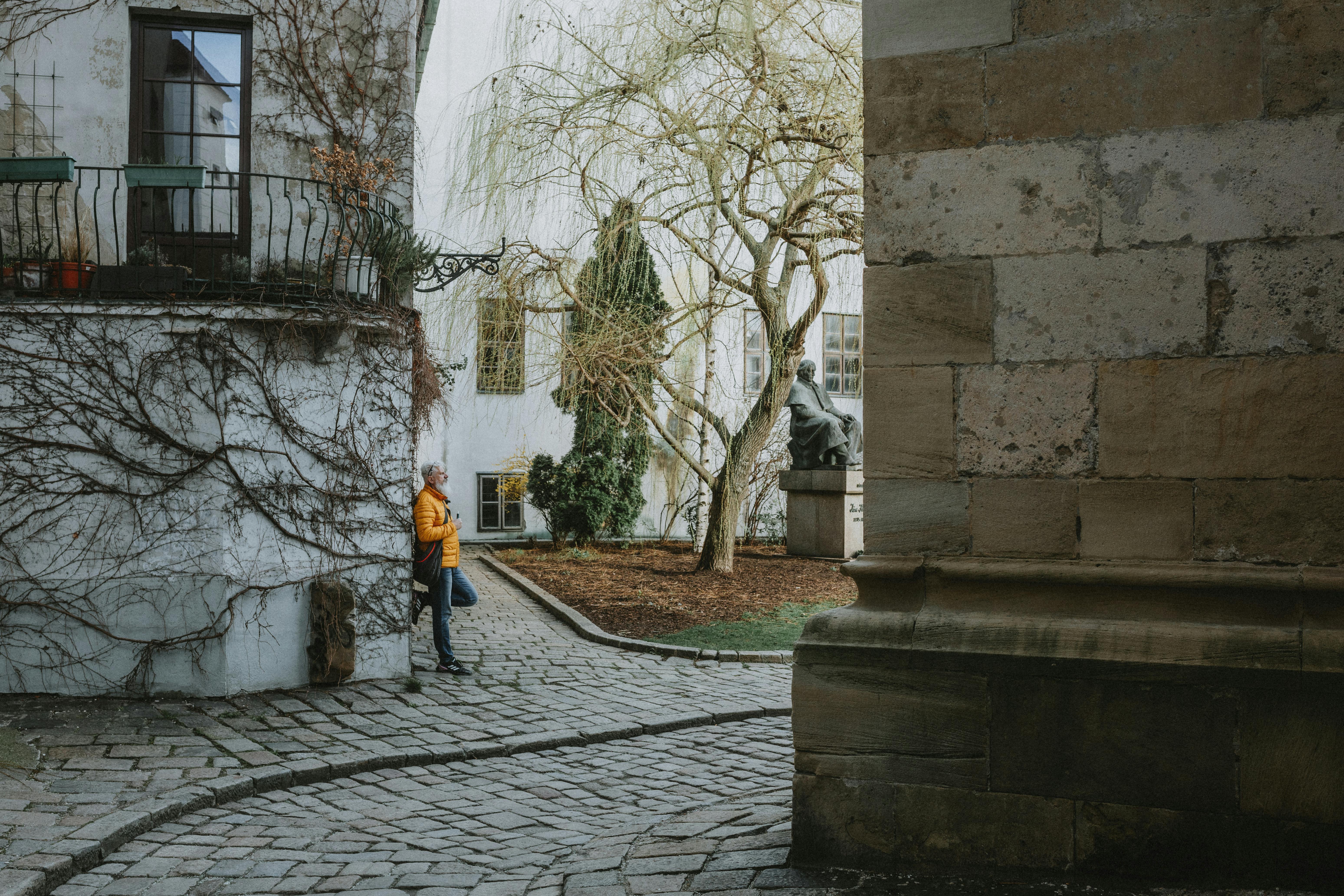 Old Man Leaning against Building Covered in Ivy · Free Stock Photo