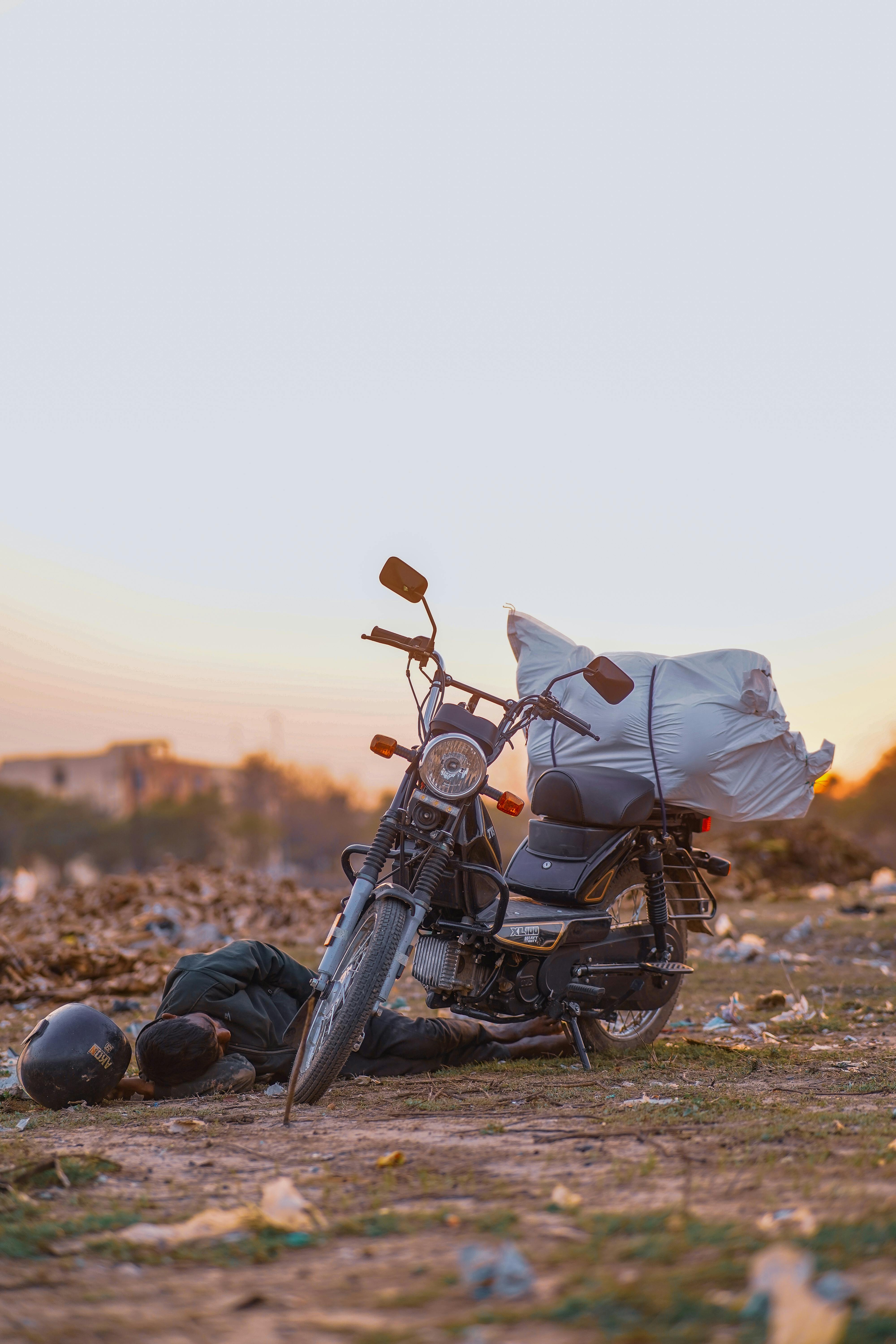 Man Lying Down under Motorbike on Field and Sleeping · Free Stock Photo