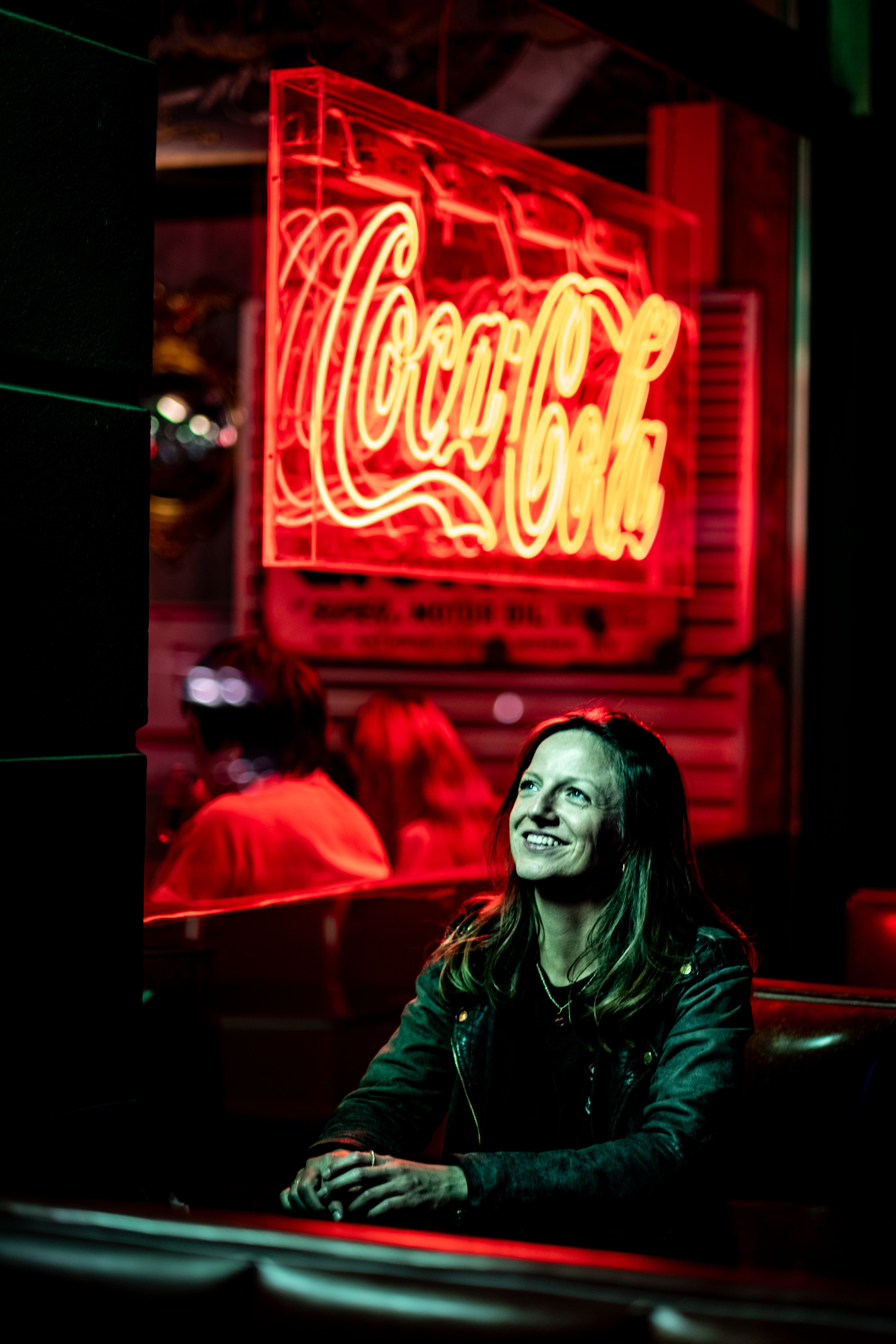 A woman sitting in front of a neon sign · Free Stock Photo
