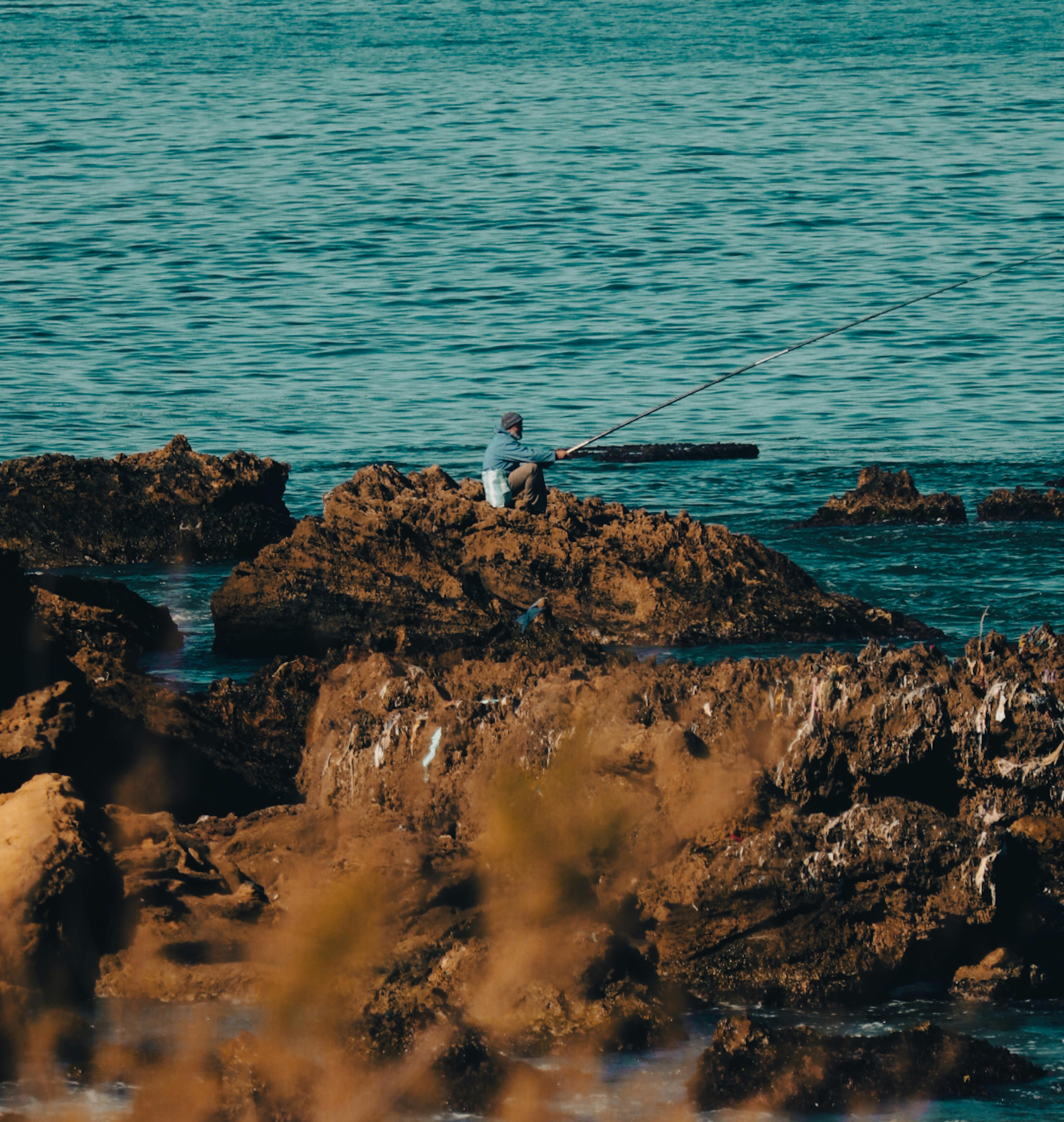 A man fishing on rocks in the ocean · Free Stock Photo