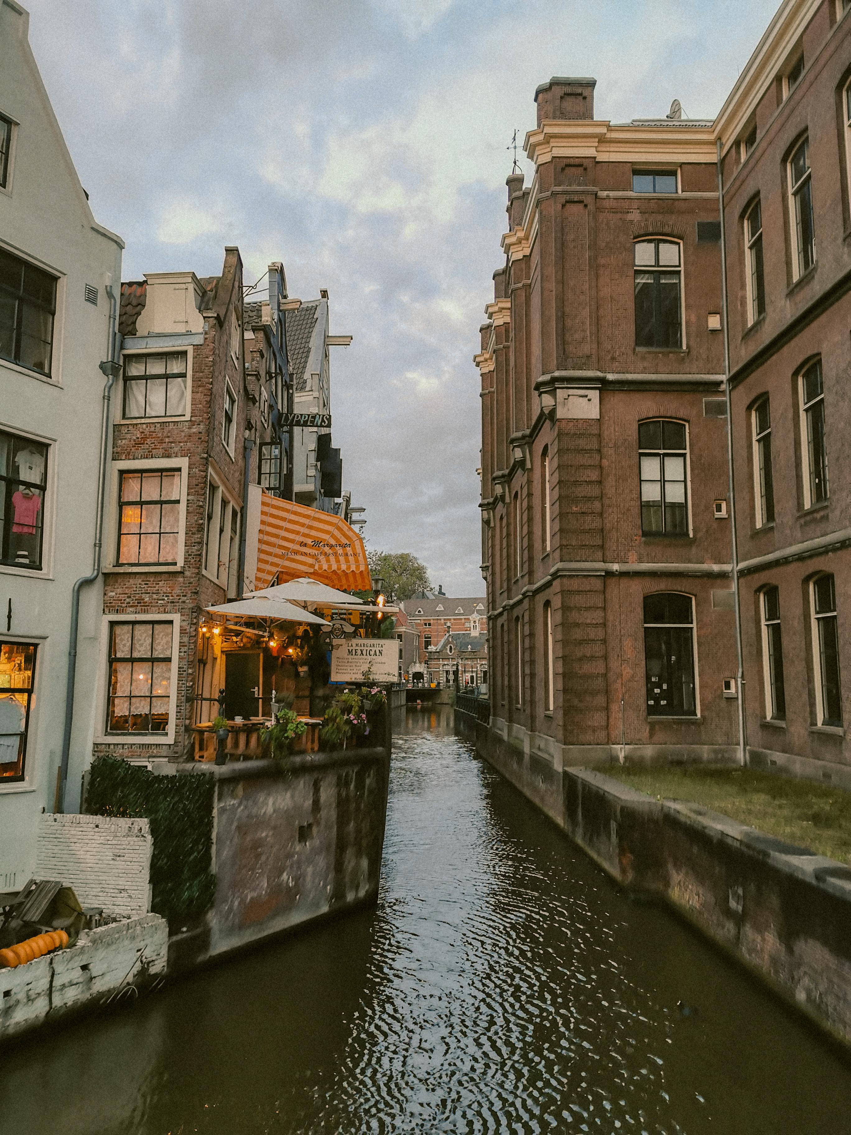 River Canal Streaming Between Buildings in Amsterdam · Free Stock Photo