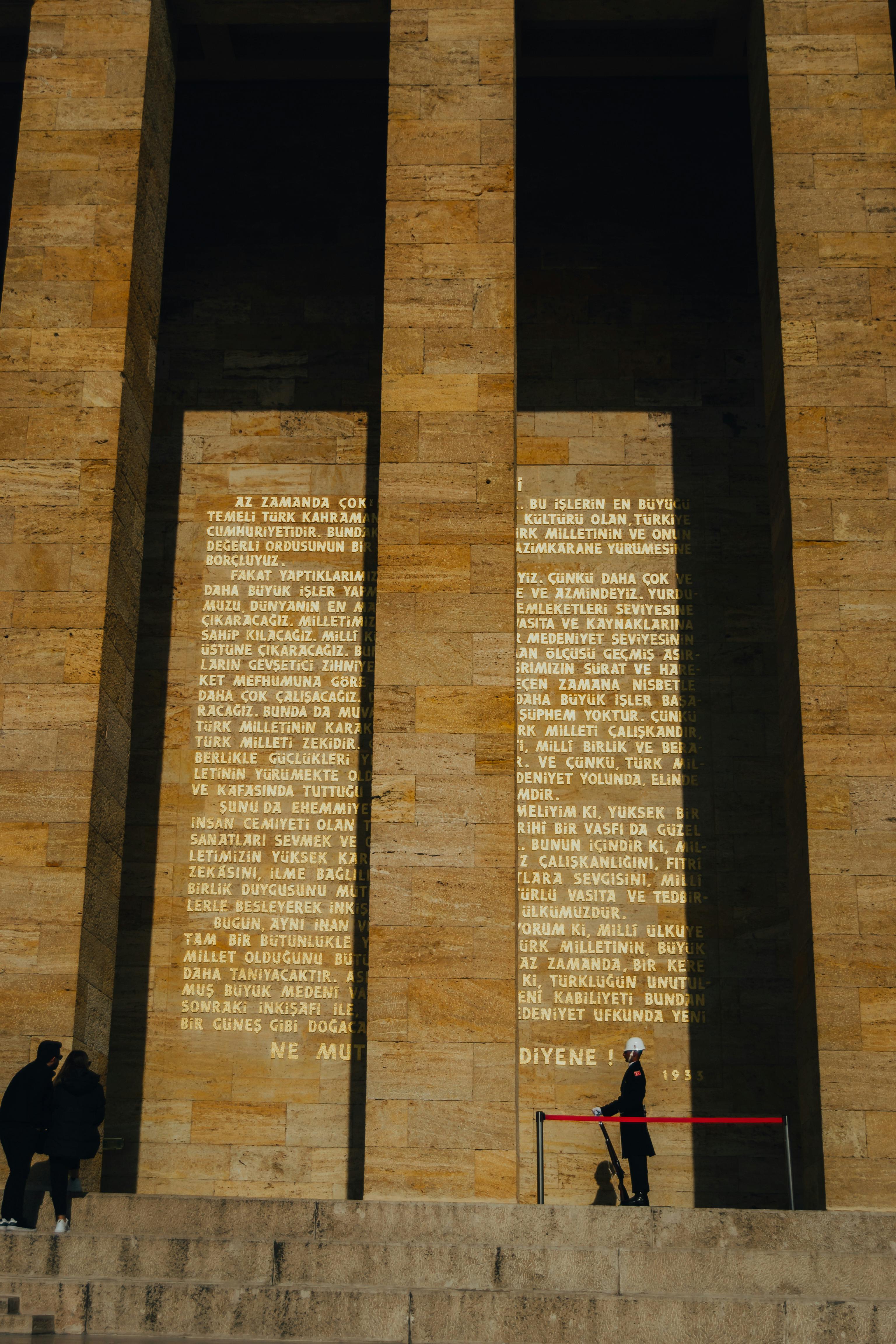 Two people walking past a large stone monument · Free Stock Photo