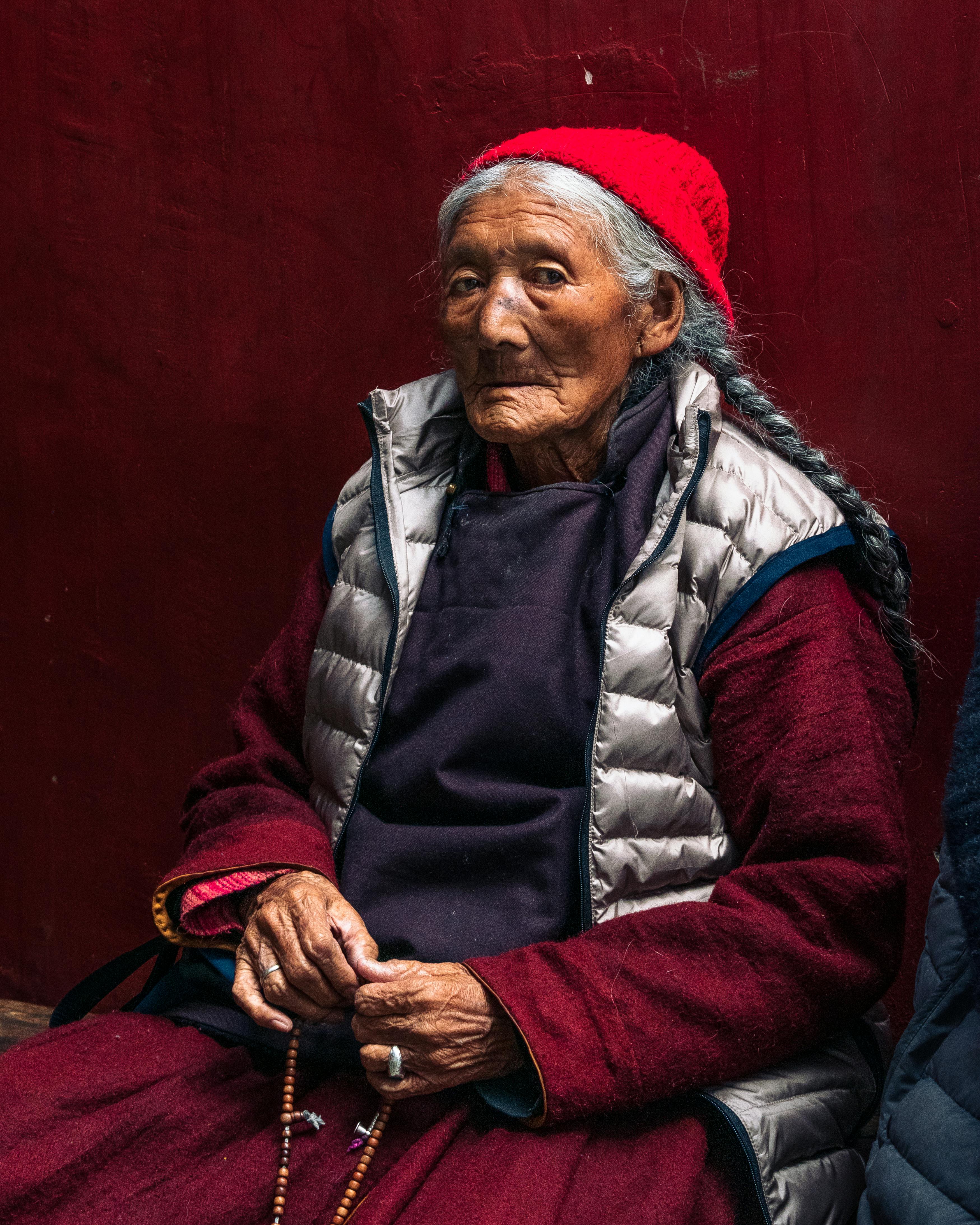 Elderly Woman in Warm Clothes Holding a Rosary and Sitting by a Red ...