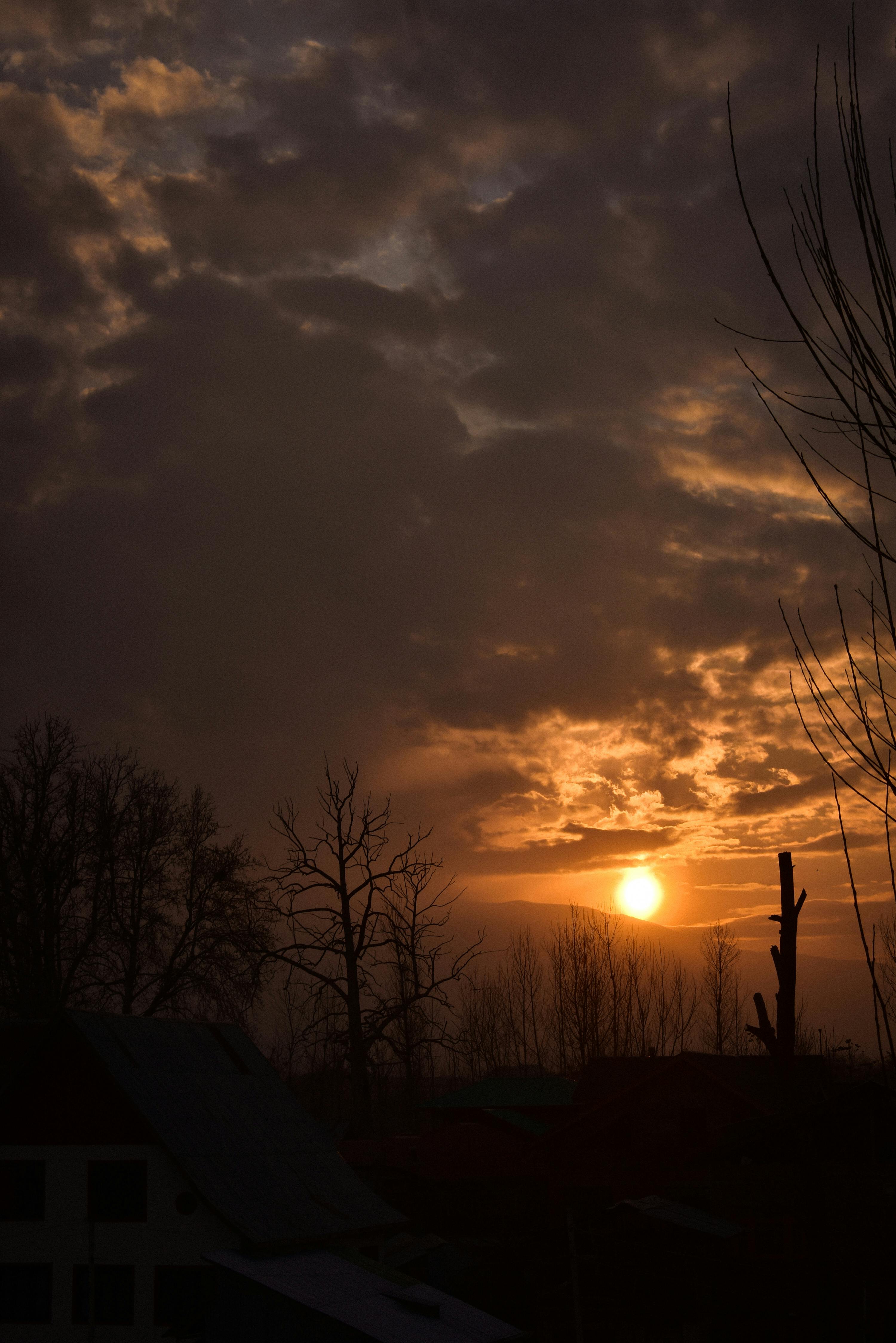 Sunset Visible through Cloudy Sky over Trees and Hills · Free Stock Photo