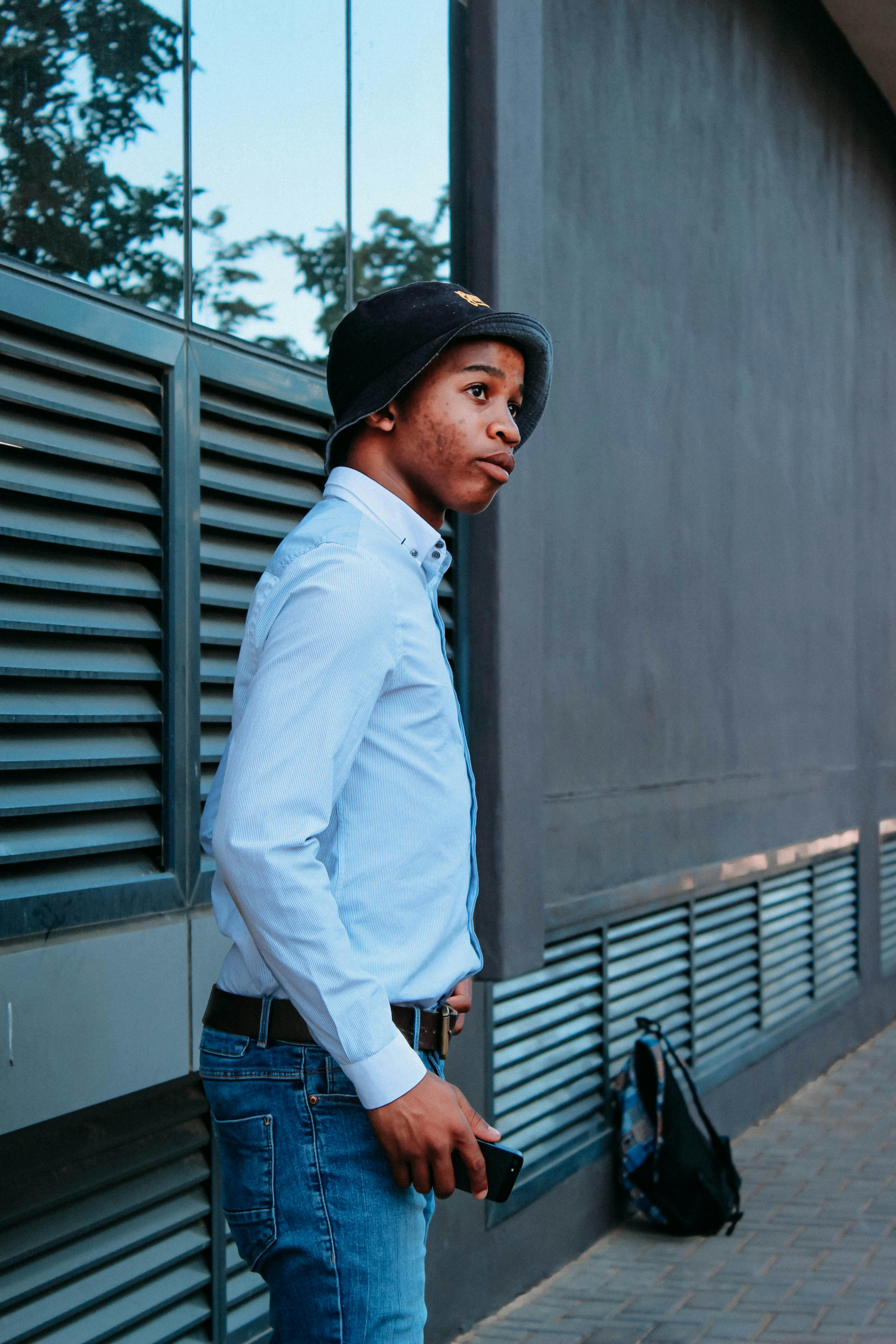 Man Standing Near Building Beside Backpack on Floor · Free Stock Photo