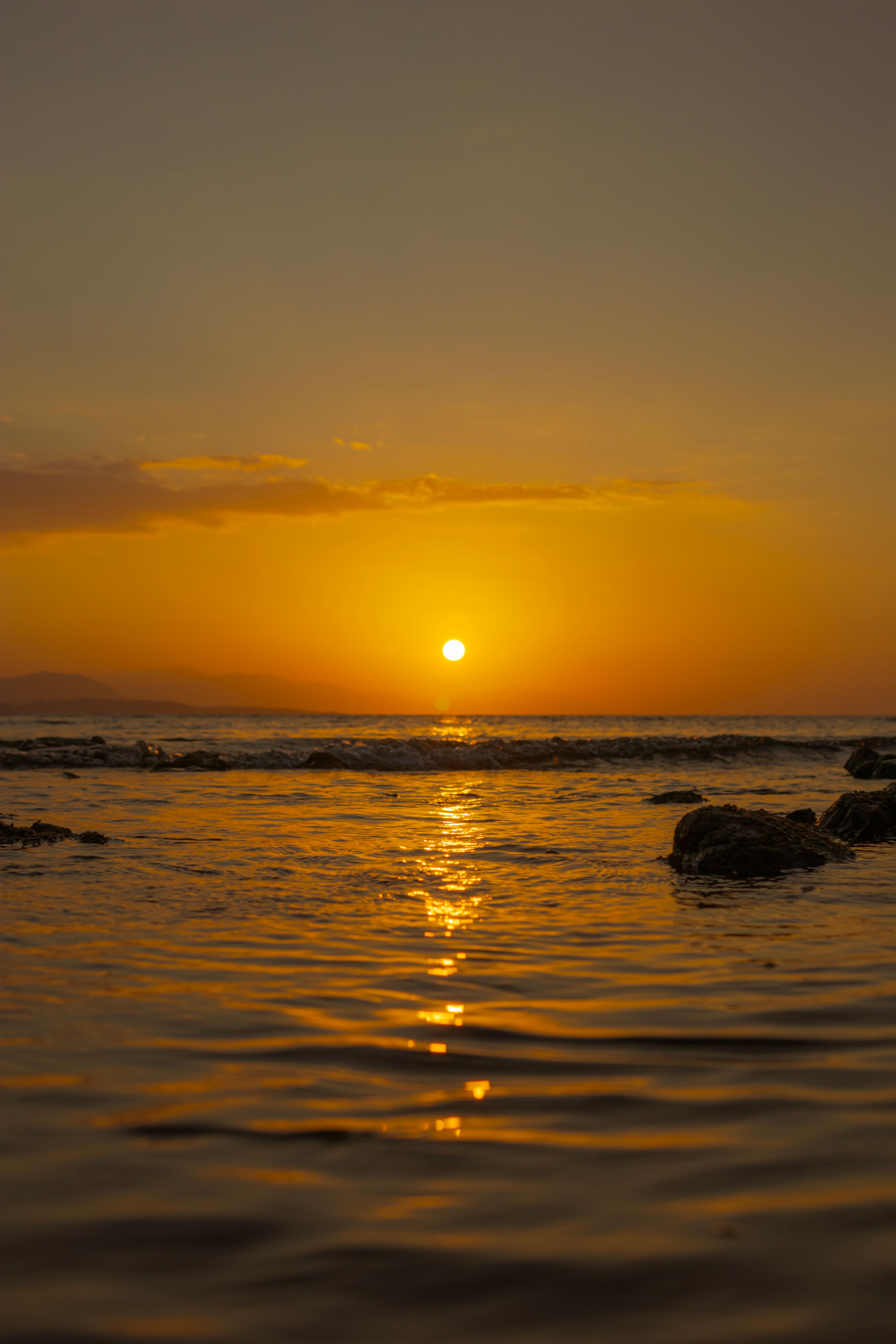 A sunset over the ocean with rocks in the water · Free Stock Photo