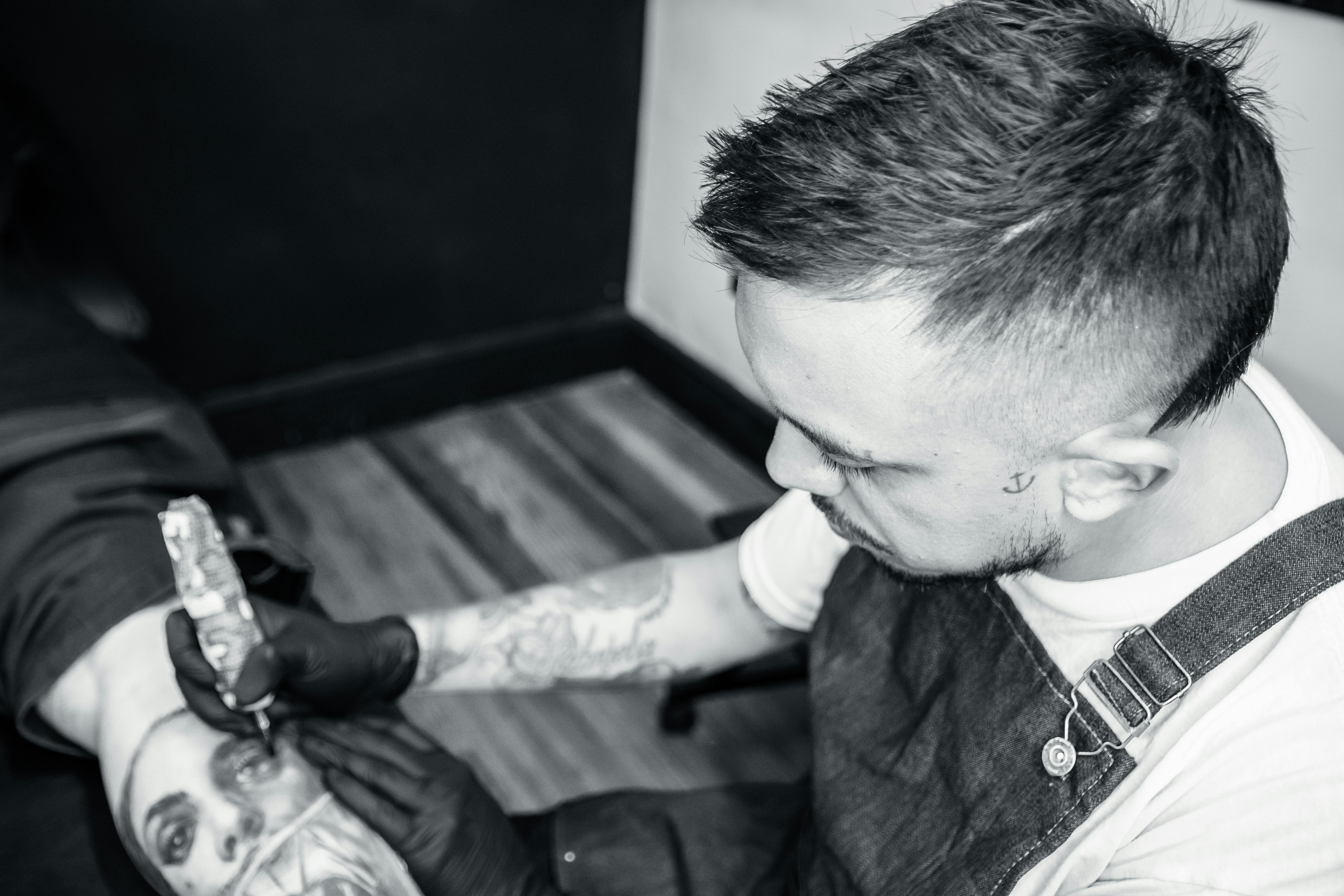Black and White Photograph of a Man Tattooing a Hand · Free Stock Photo