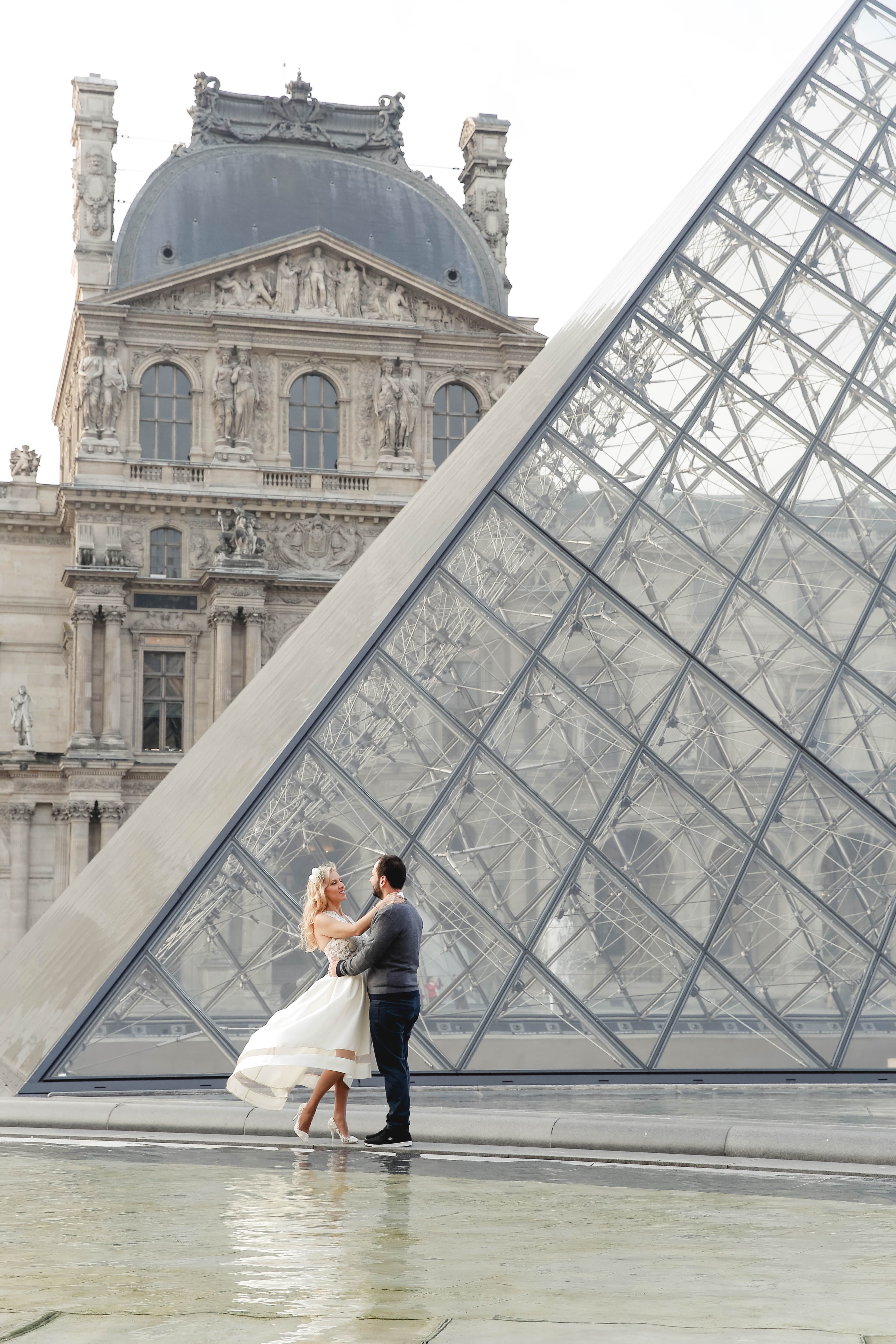 Newlyweds Embracing in Front of the Louvre Pyramid · Free Stock Photo