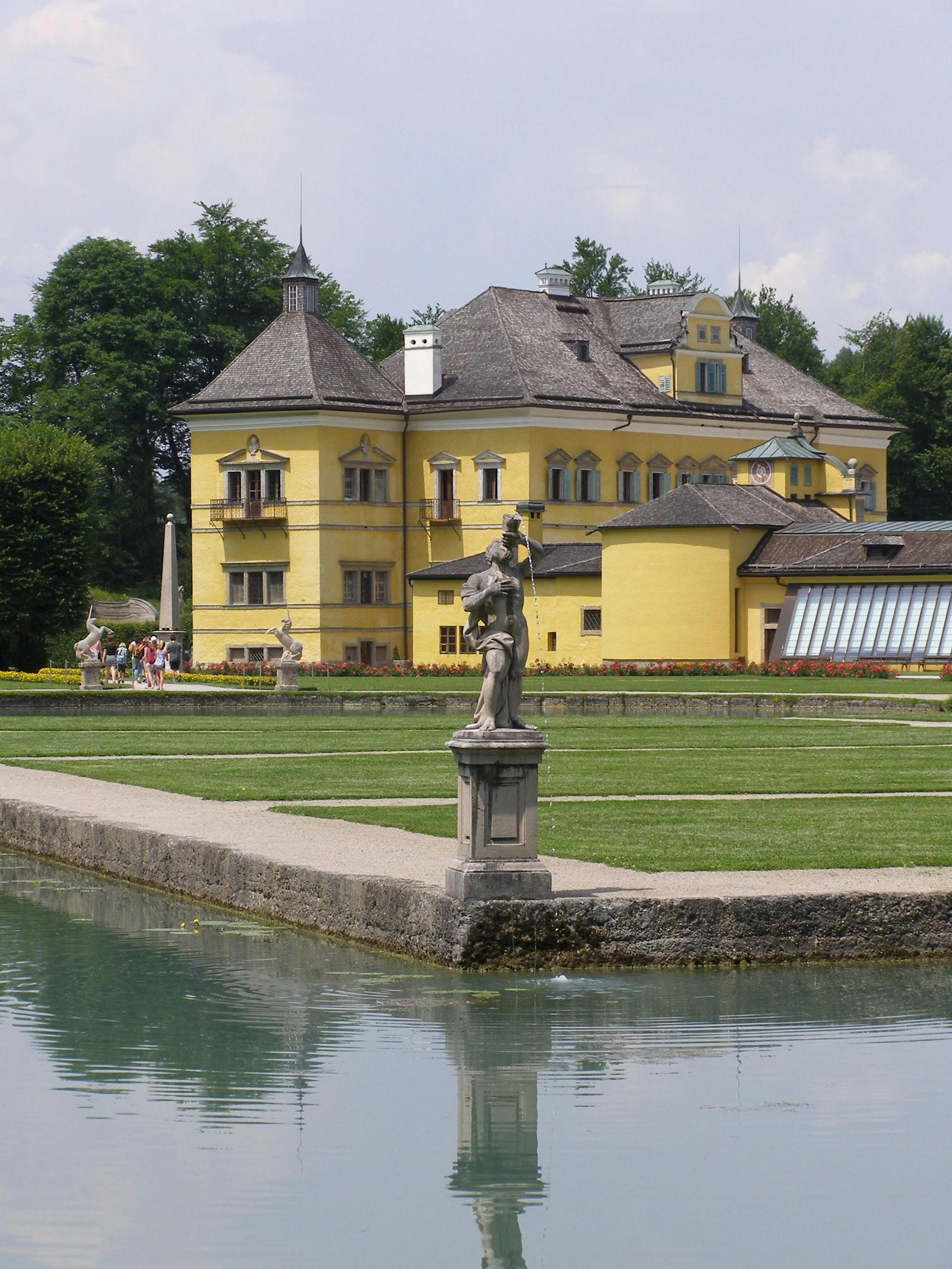 A statue is in front of a large yellow house · Free Stock Photo
