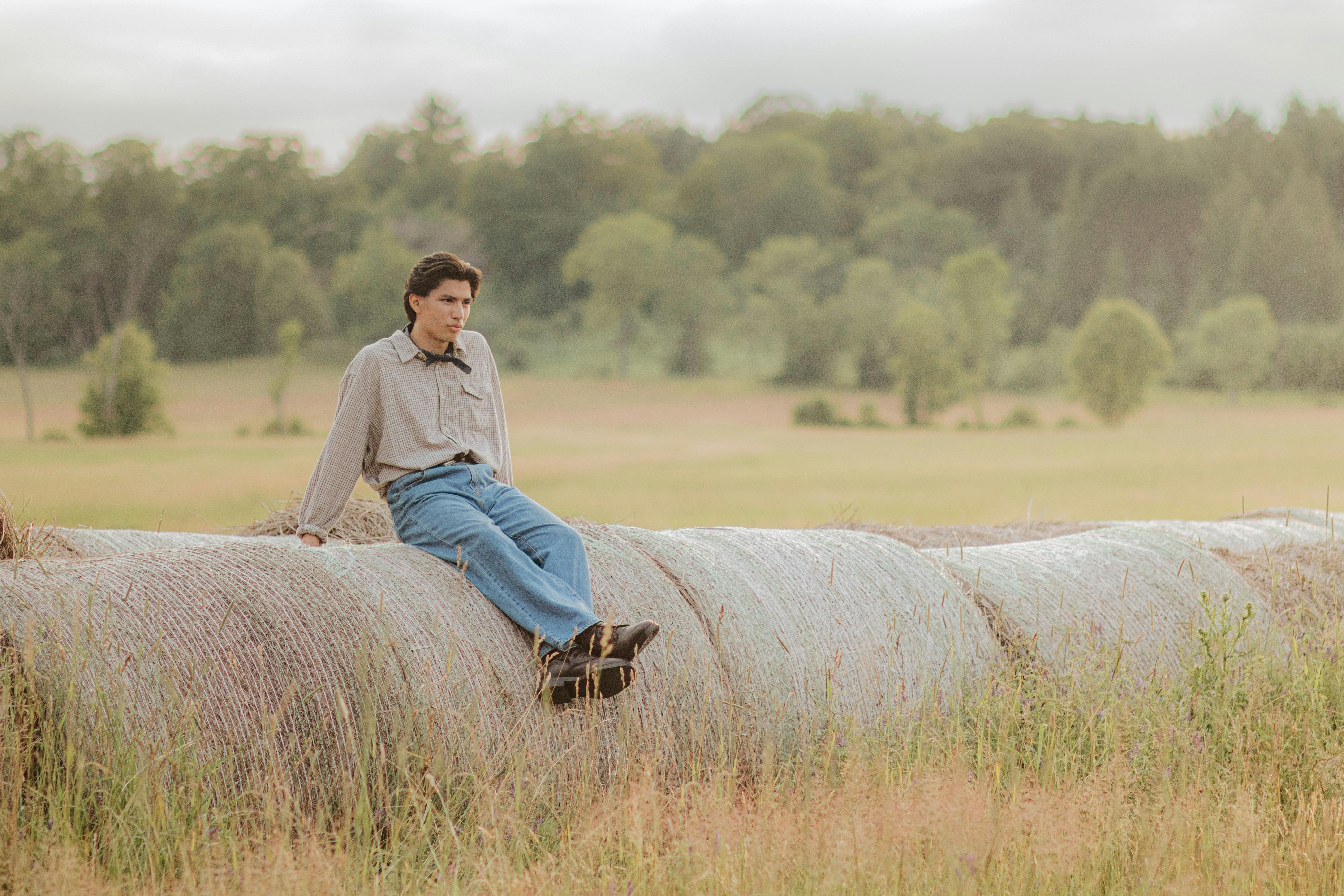 Man in Shirt Sitting on Hay Bales in Countryside · Free Stock Photo