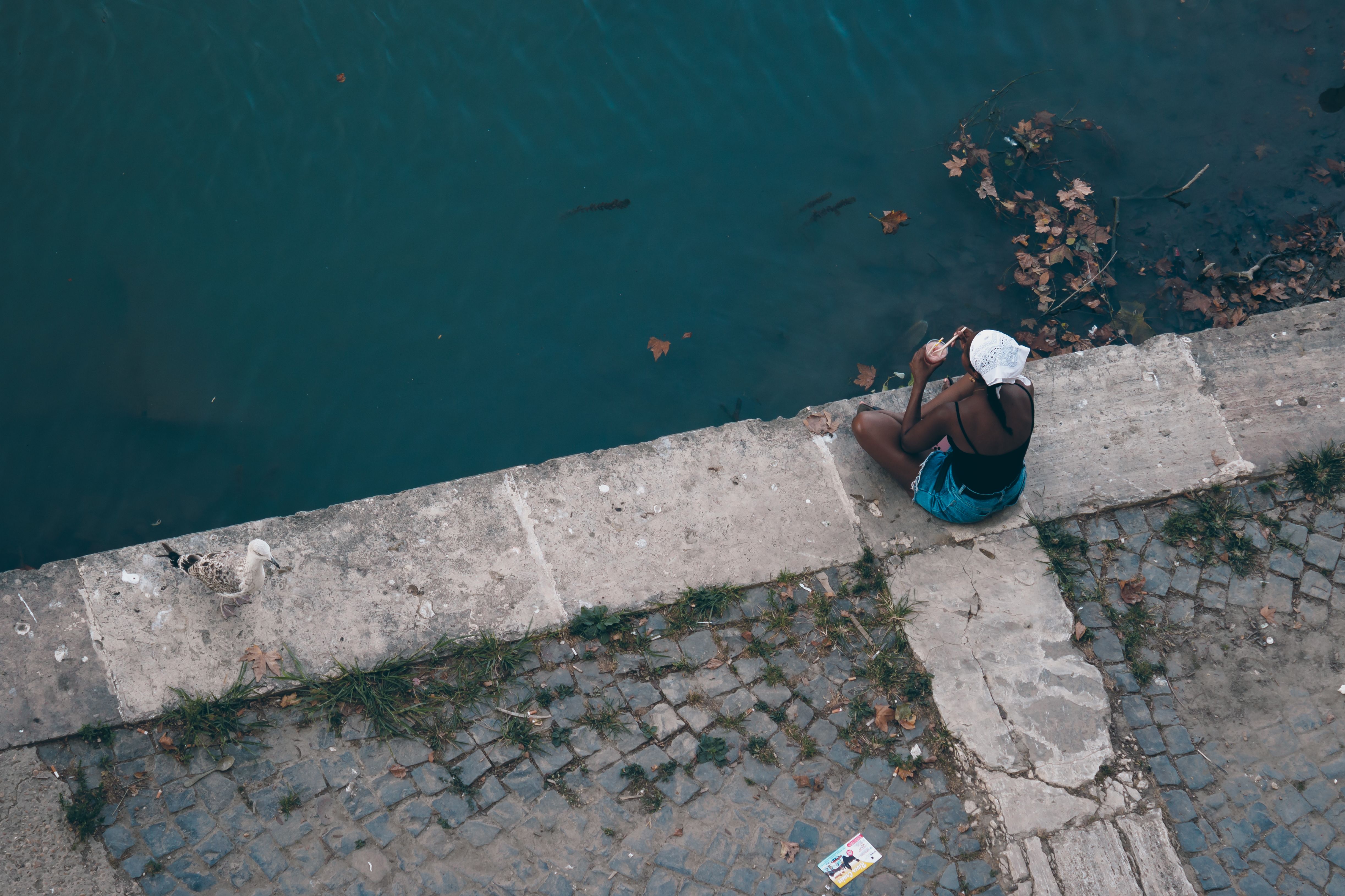 A person sitting on a ledge looking at the water · Free Stock Photo