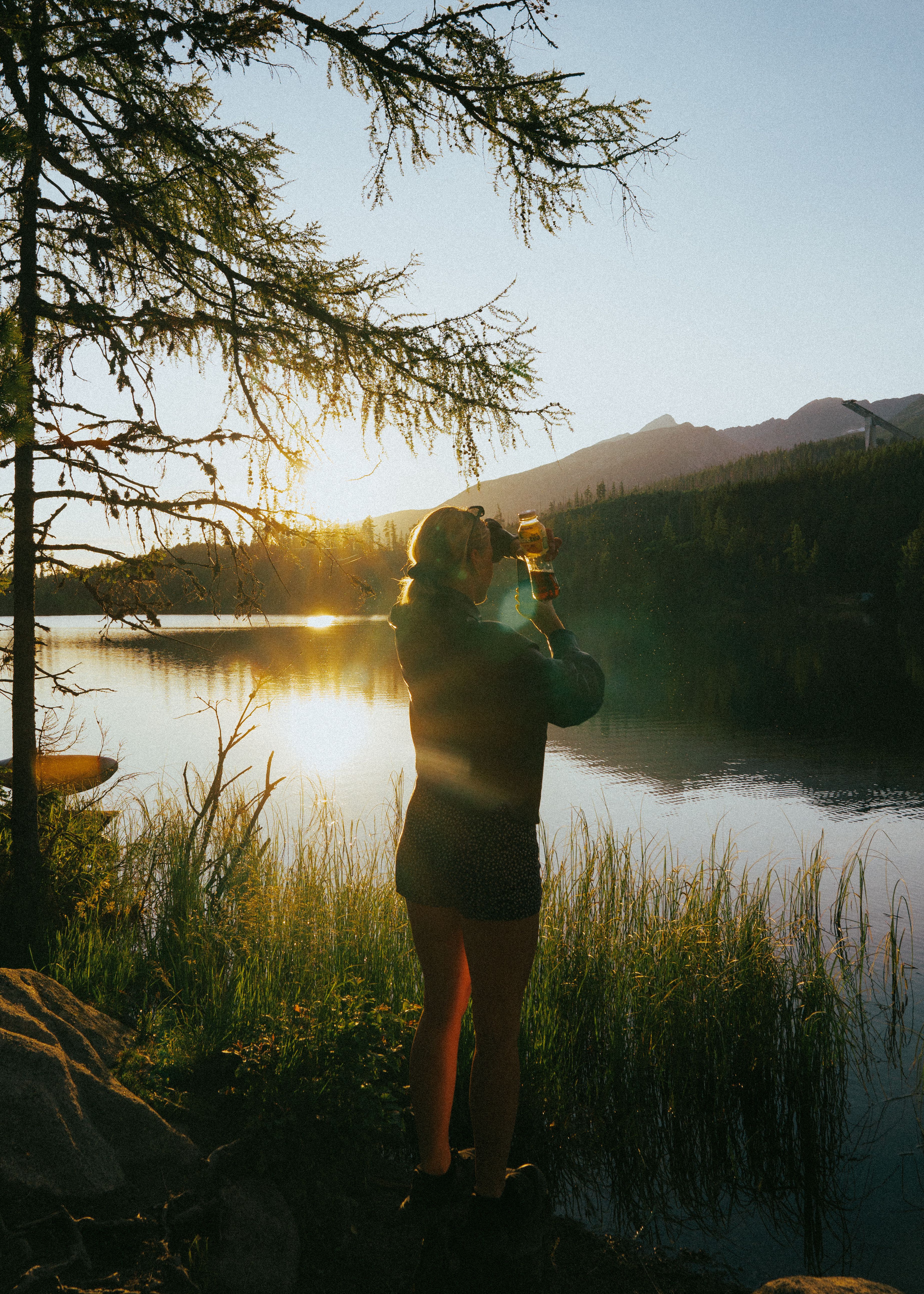 A woman taking a photo of the sun setting over a lake · Free Stock Photo