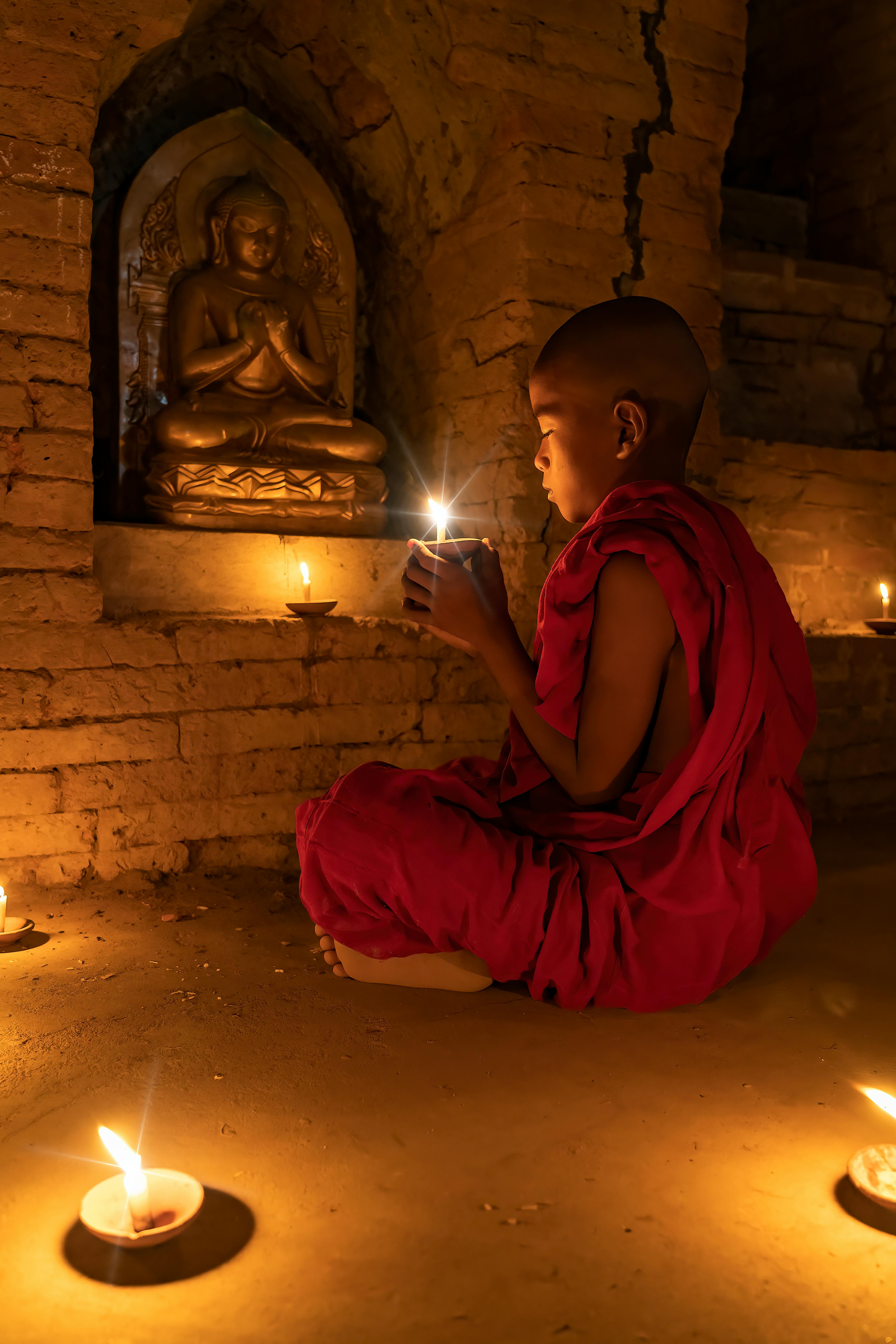 Boy in Monk Robes Sitting with Burning Candles by Buddha Statue · Free ...