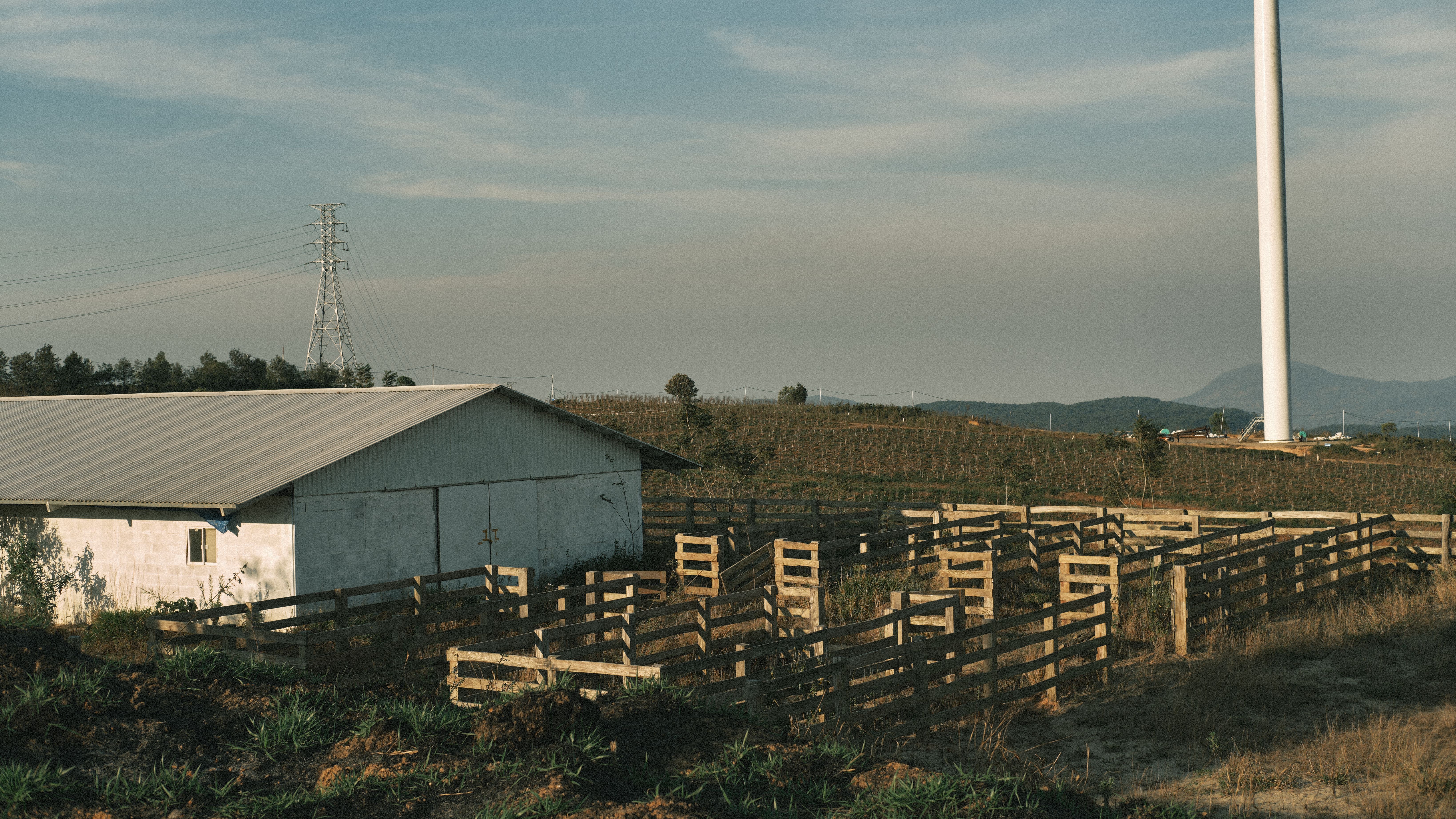 A wind turbine in the distance with a barn and fence · Free Stock Photo