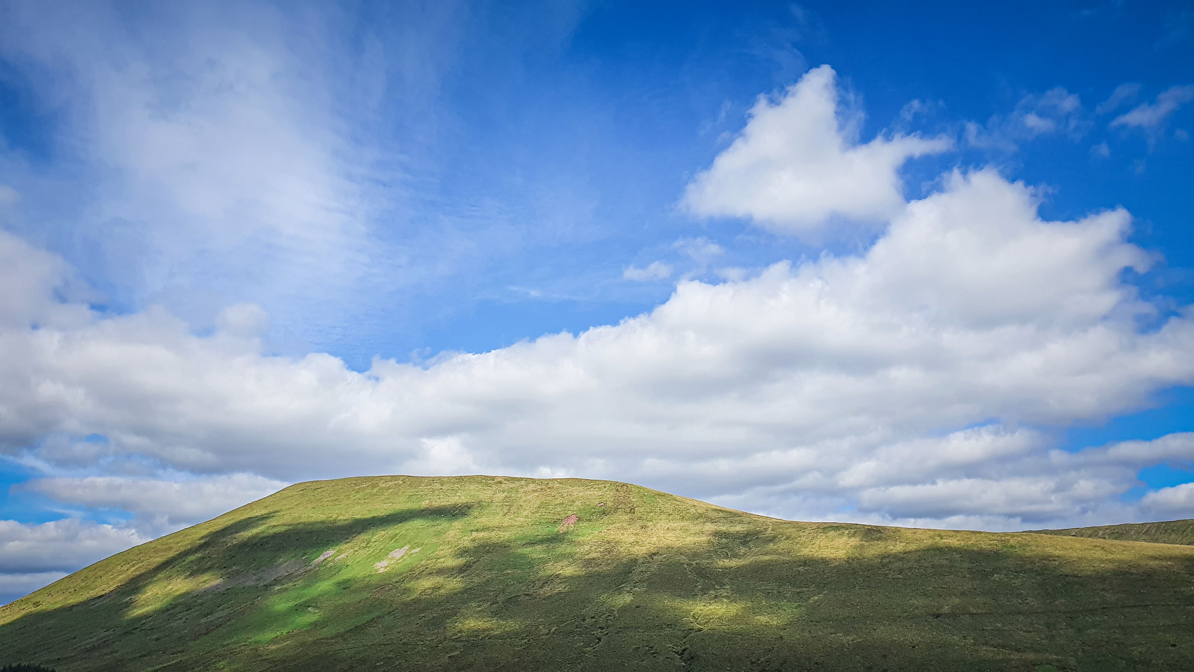 A grassy hill with clouds in the sky · Free Stock Photo