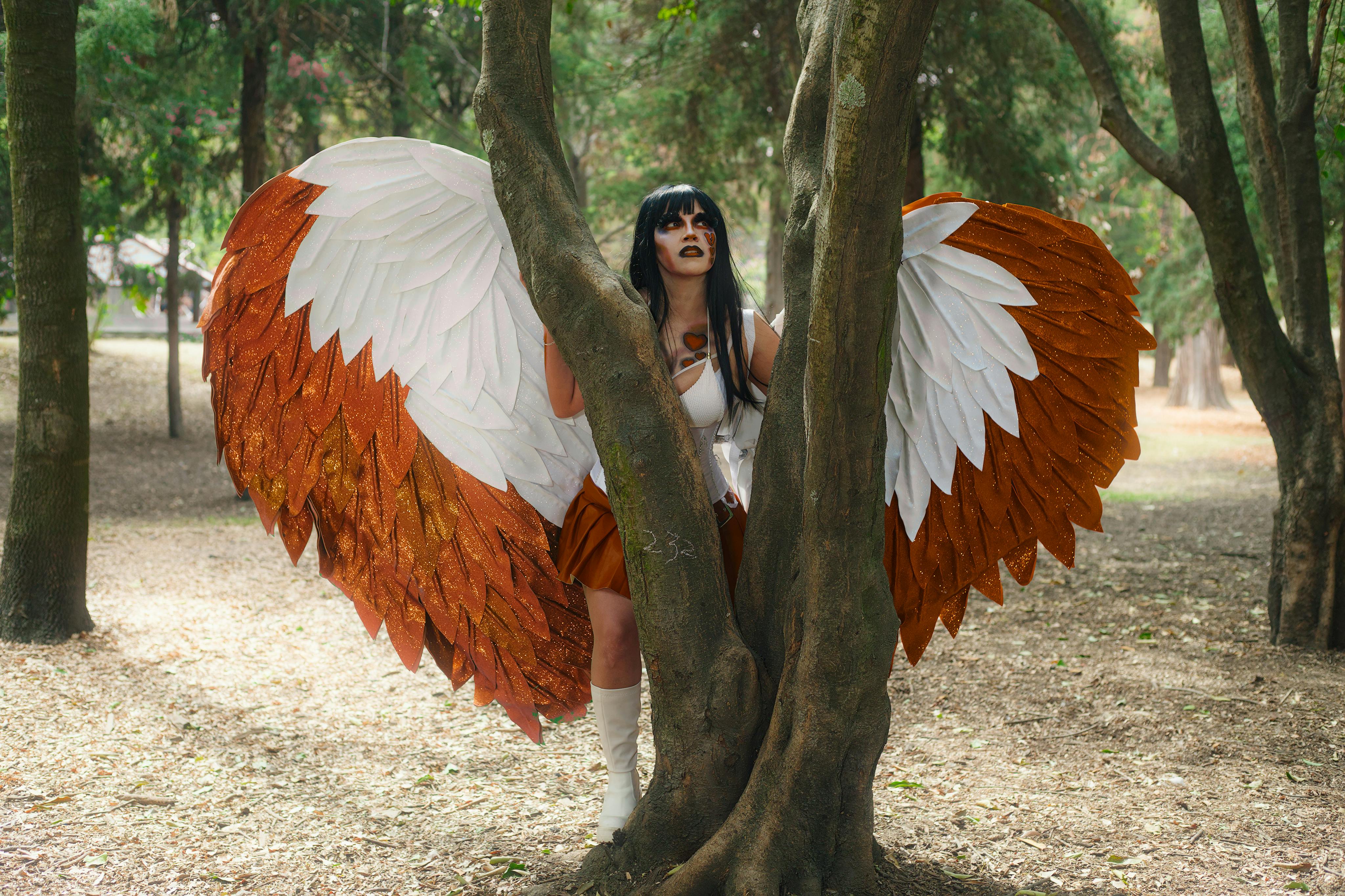 Woman in Cosplay Angel Costume Standing behind Trees · Free Stock Photo