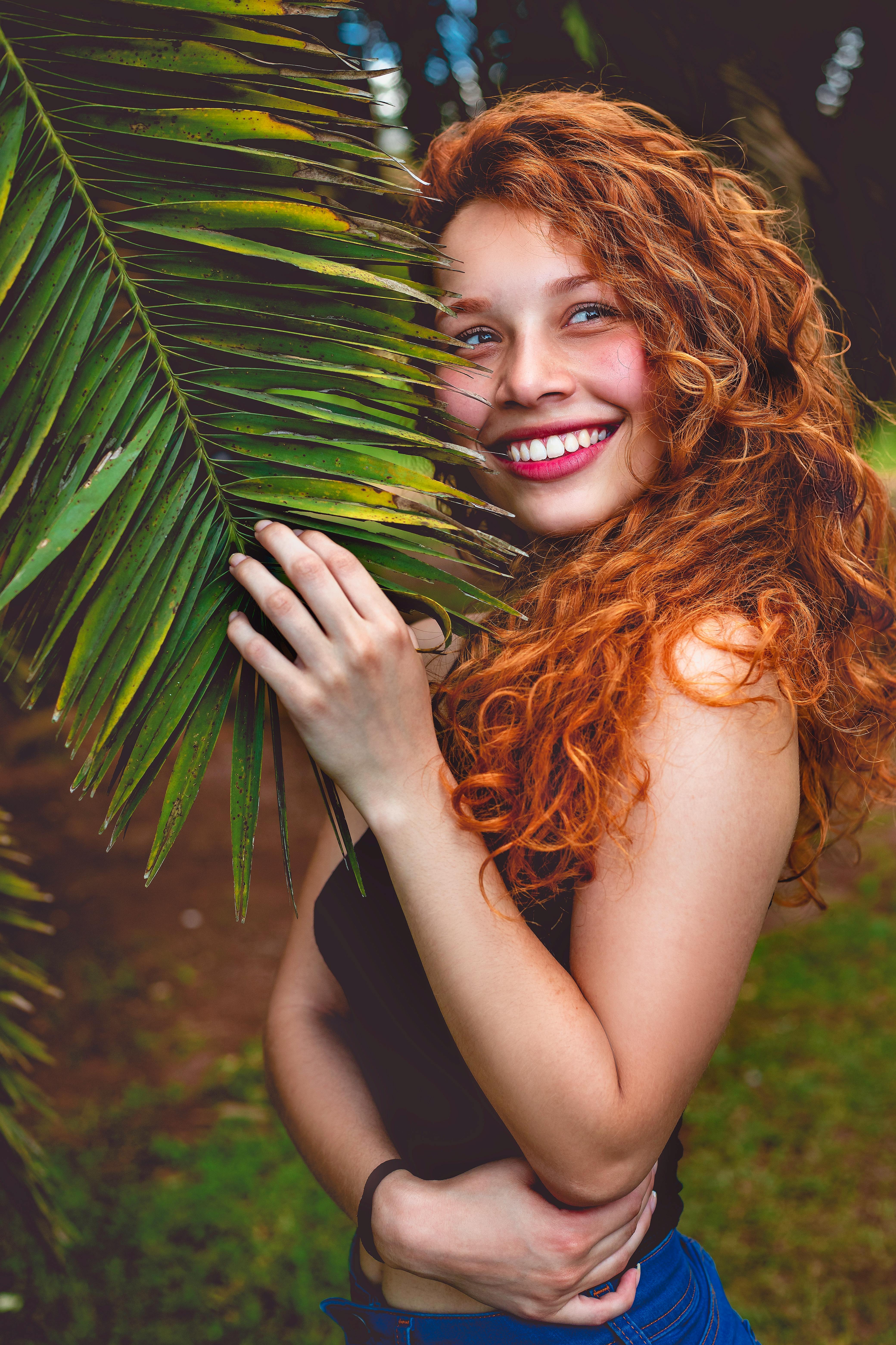 Smiling Woman Standing Near Palm Tree Holding Its Leaf · Free Stock Photo