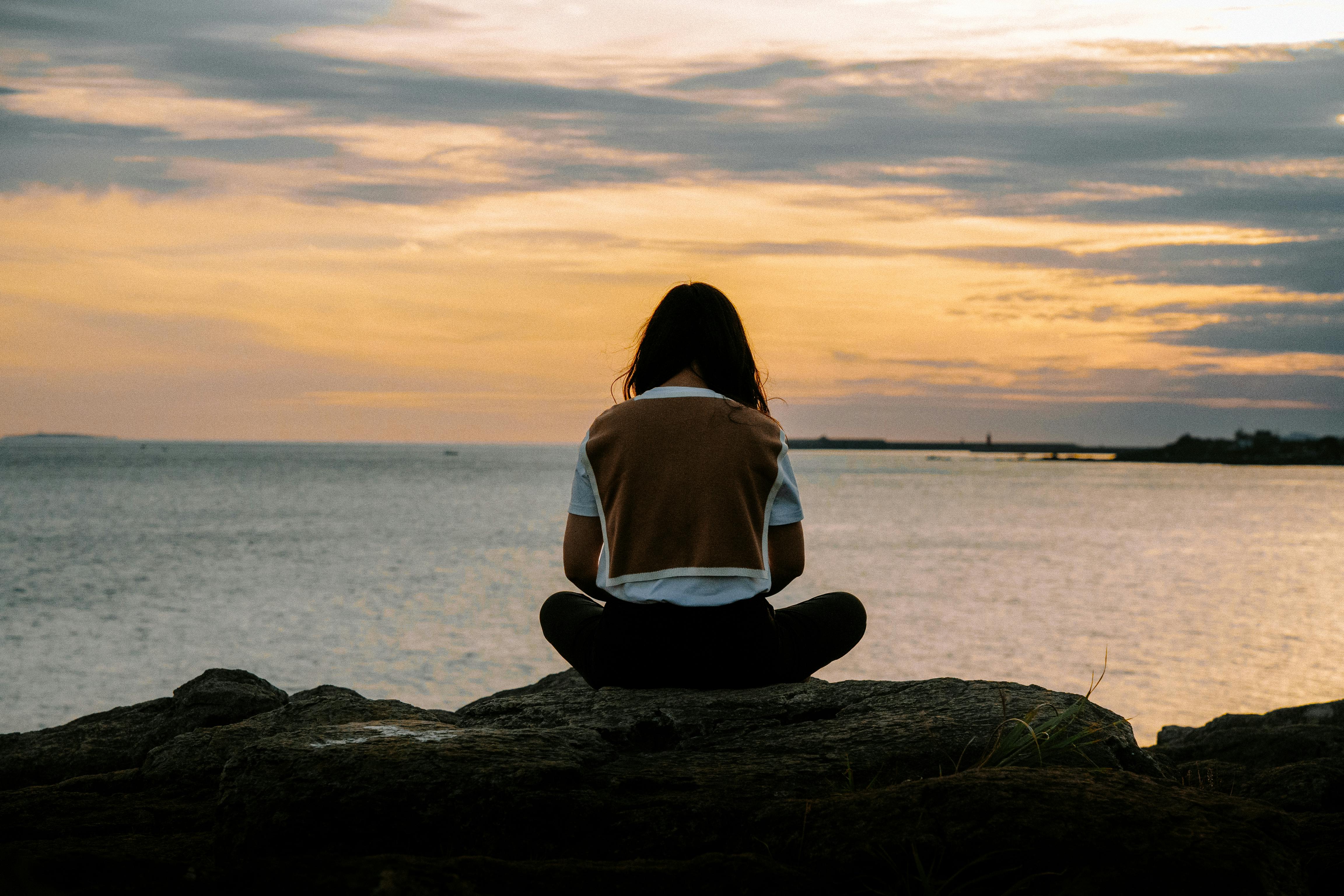 Back View of Woman Sitting on Rocks on Sea Shore at Sunset · Free Stock ...