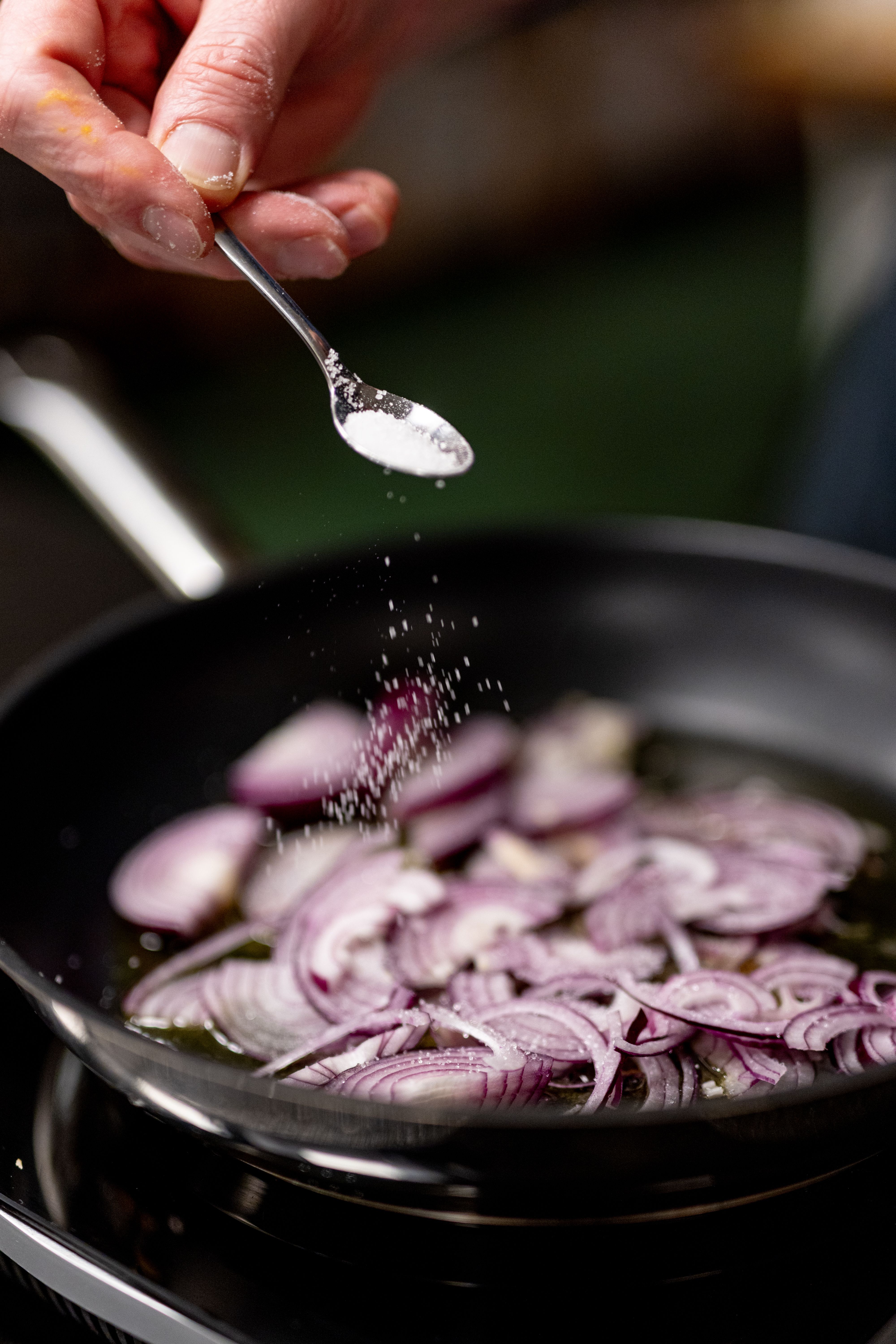A person is adding salt to onions in a frying pan · Free Stock Photo