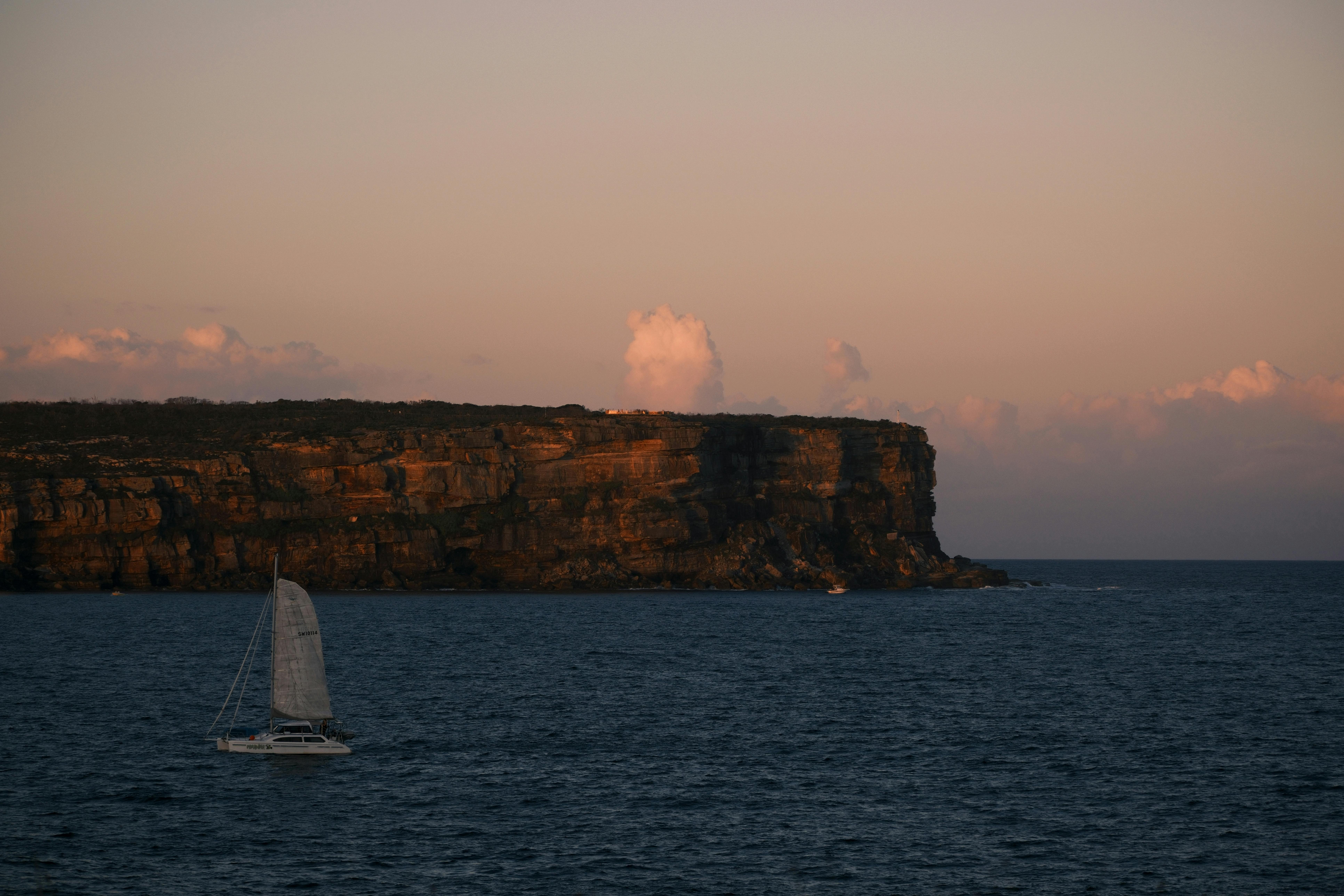 Sailboat Passing a Rocky Cliff at Sunset · Free Stock Photo