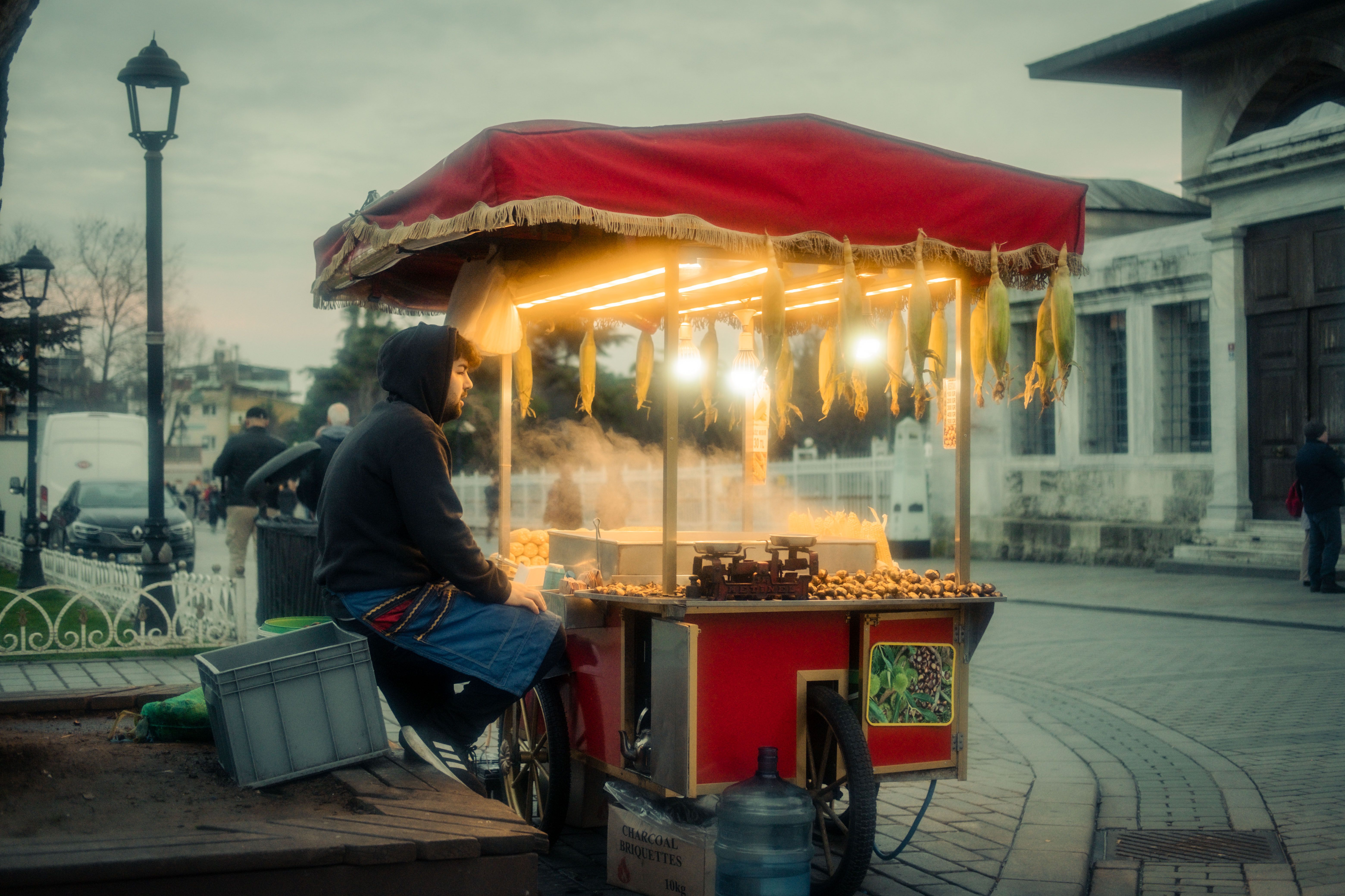 Seller Sitting behind Food Stall on Sidewalk · Free Stock Photo
