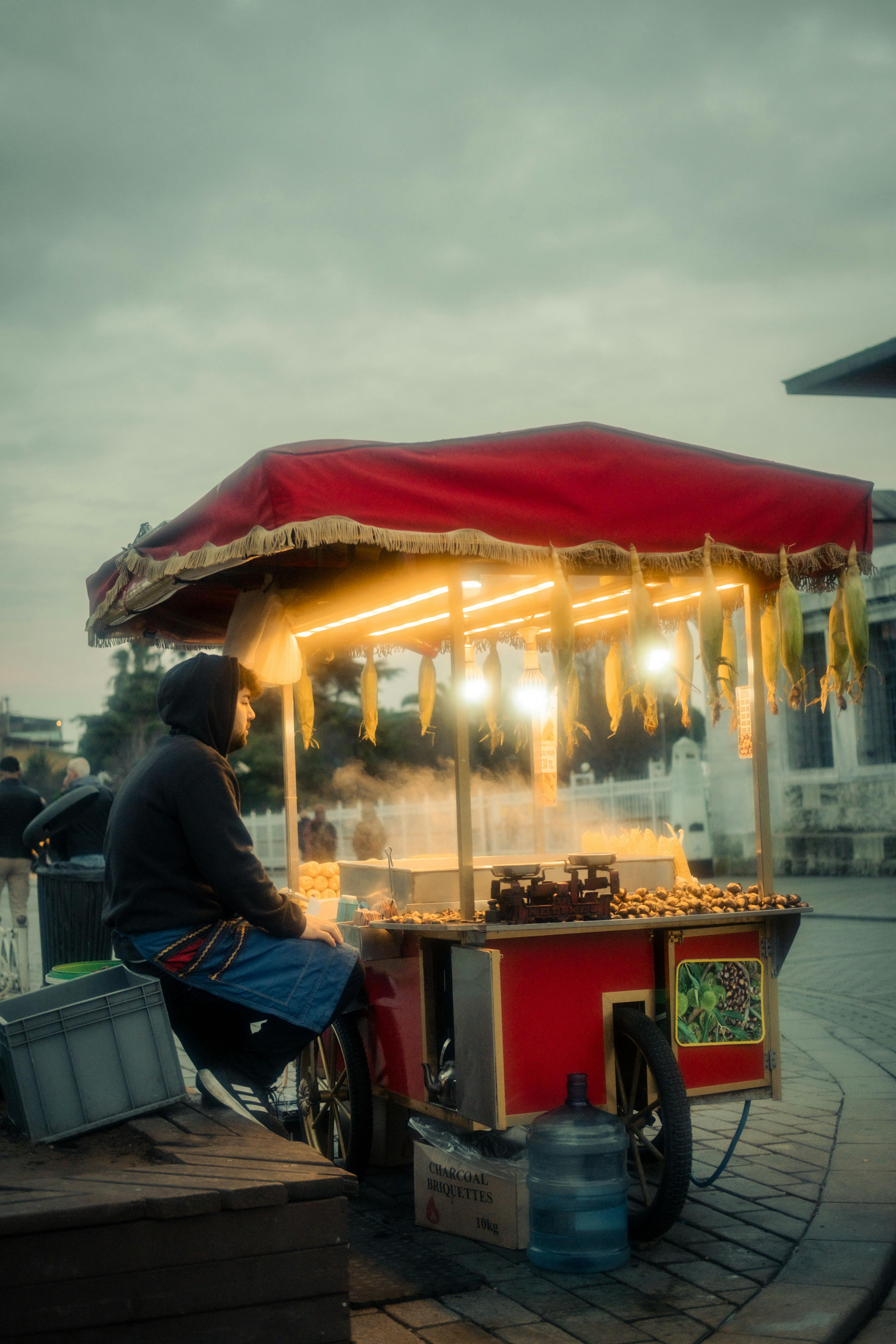 Man Sitting behind Lit Up Food Stall · Free Stock Photo