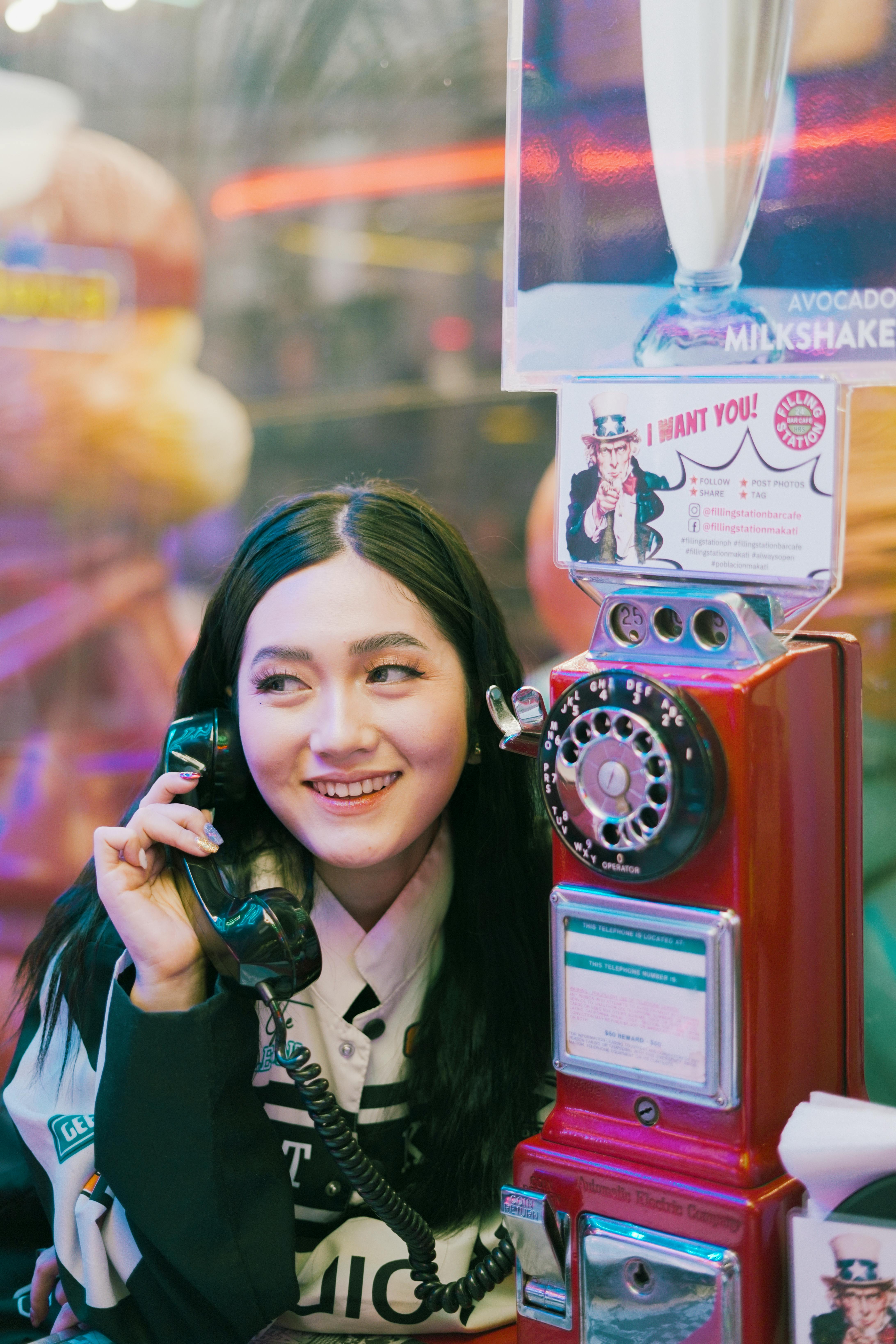 Smiling Young Woman Using a Retro Pay Phone · Free Stock Photo