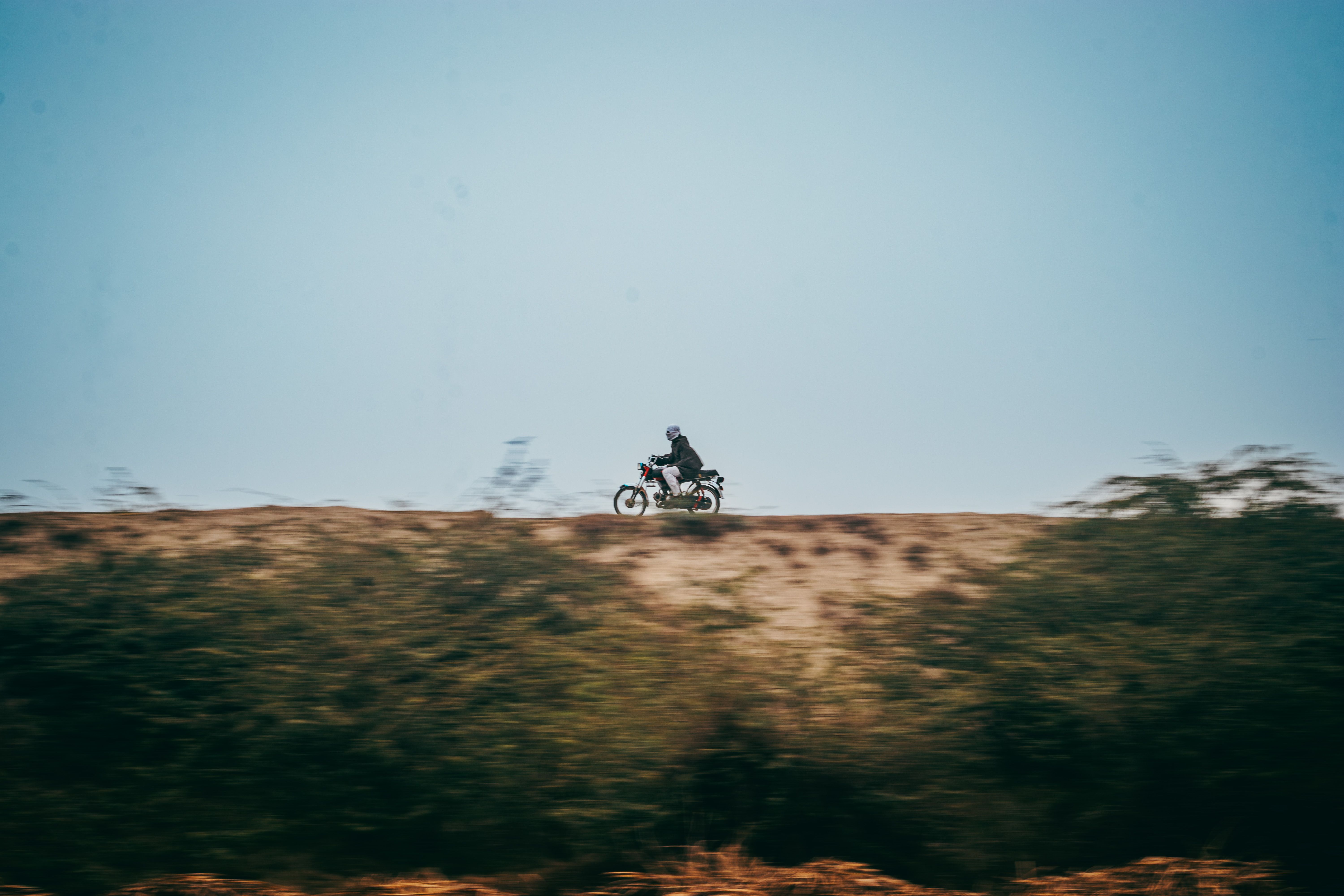 Biker Riding across Hill under Blue Sky · Free Stock Photo