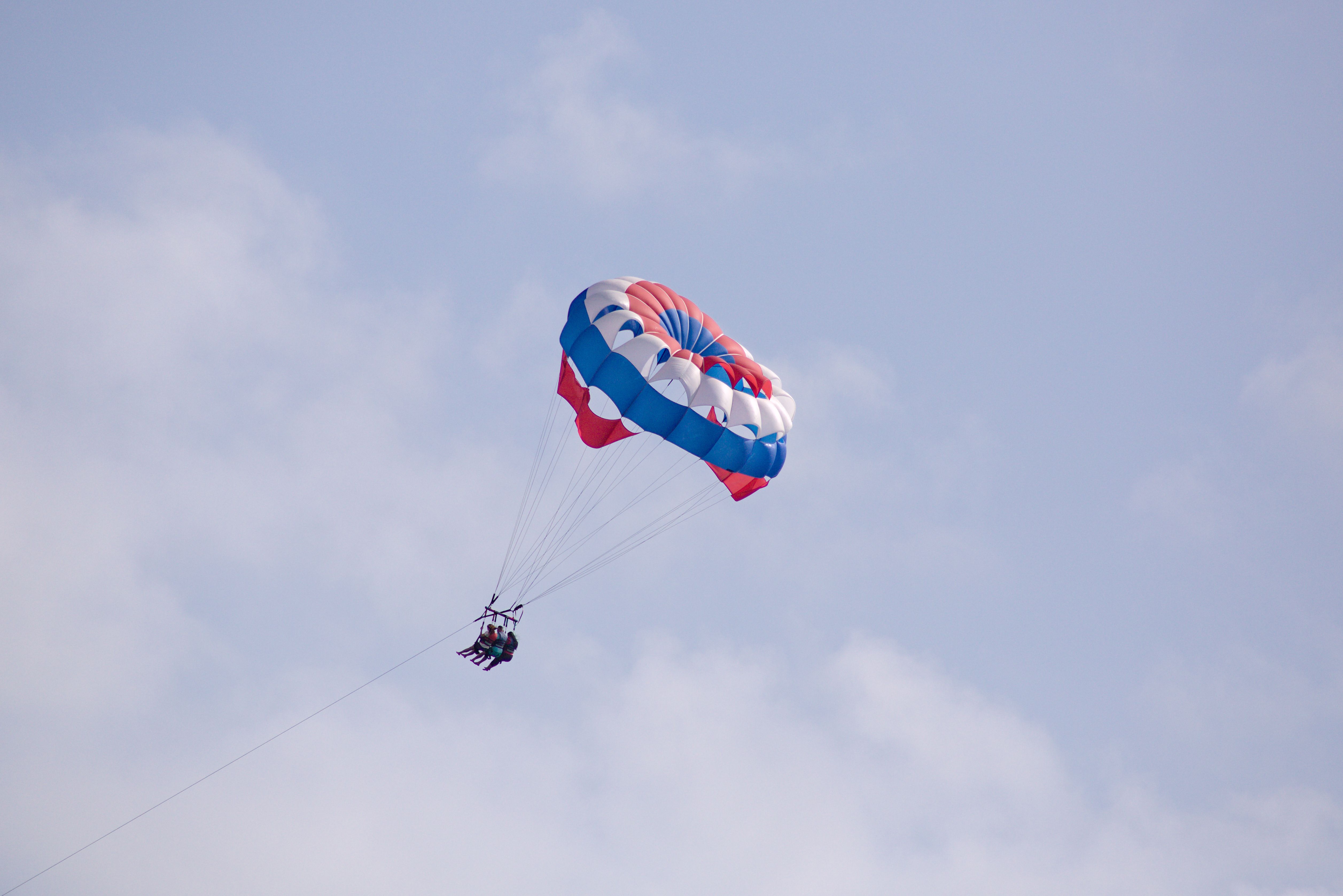 A person parasailing in the sky with a blue and red parachute · Free ...