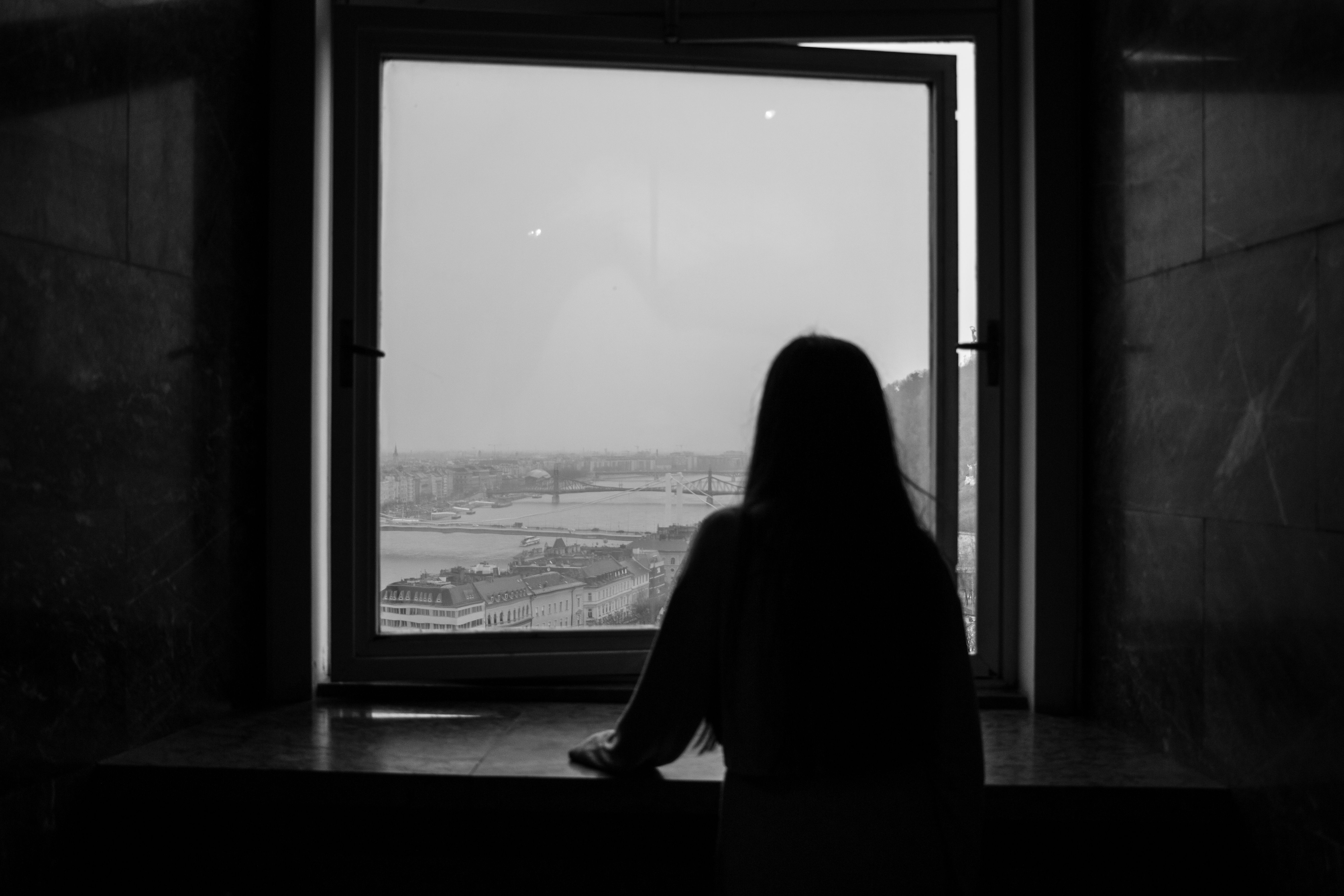 Woman Standing by Window with River in Budapest behind · Free Stock Photo