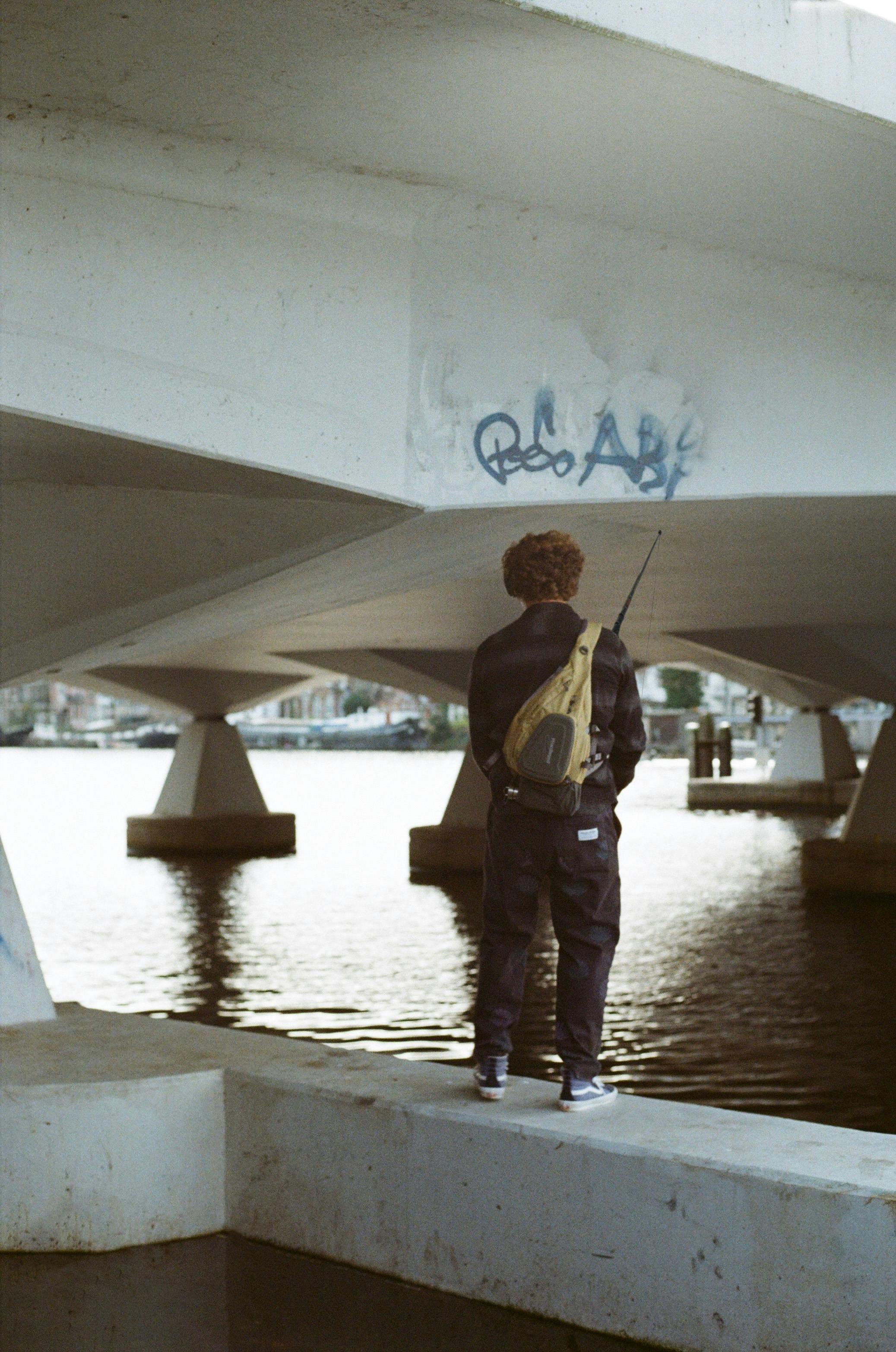 Man with Backpack Standing on Wall under Bridge · Free Stock Photo
