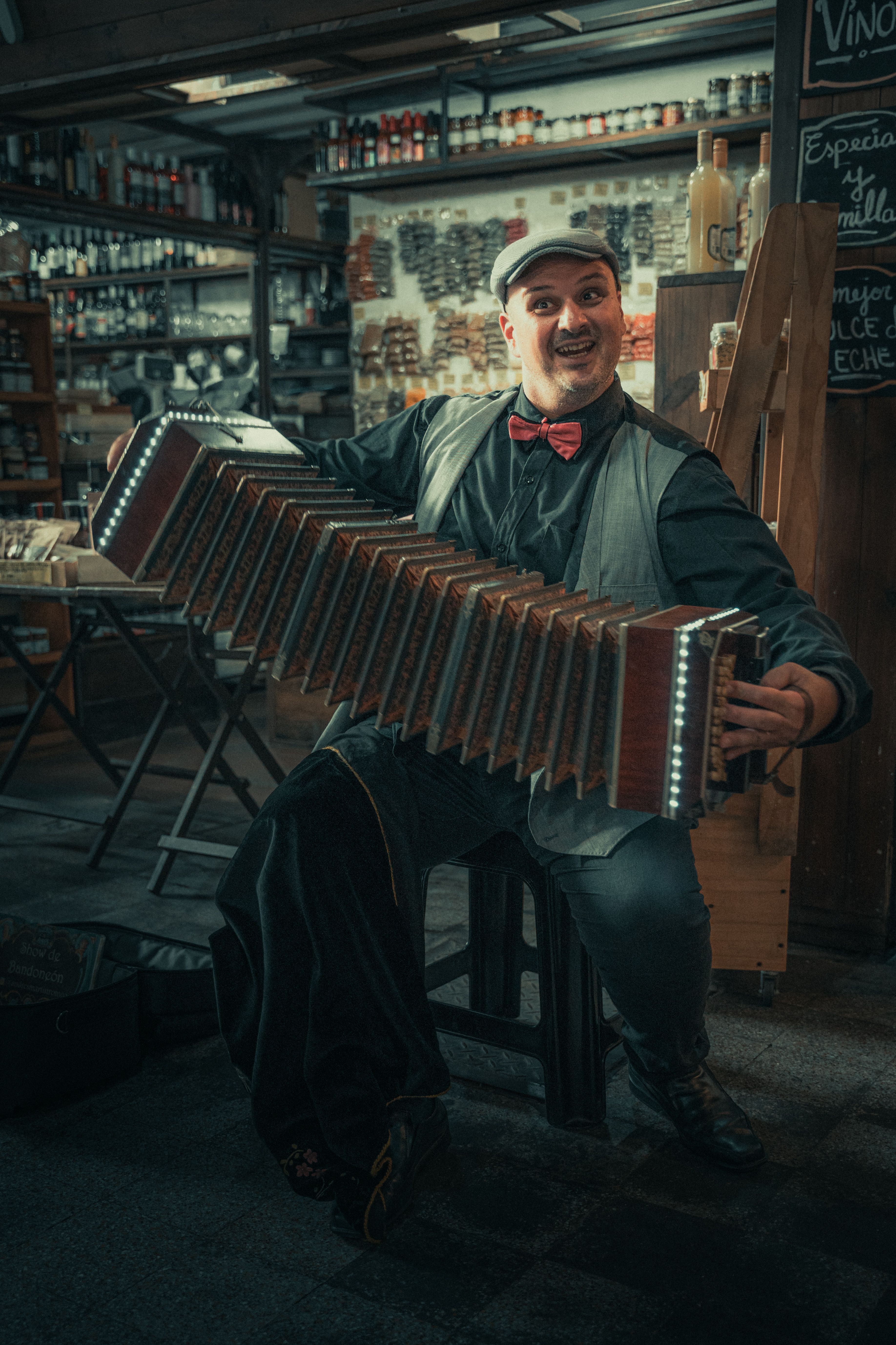 A Happy Man Holding a Bandoneon while Sitting near a Bar · Free Stock Photo
