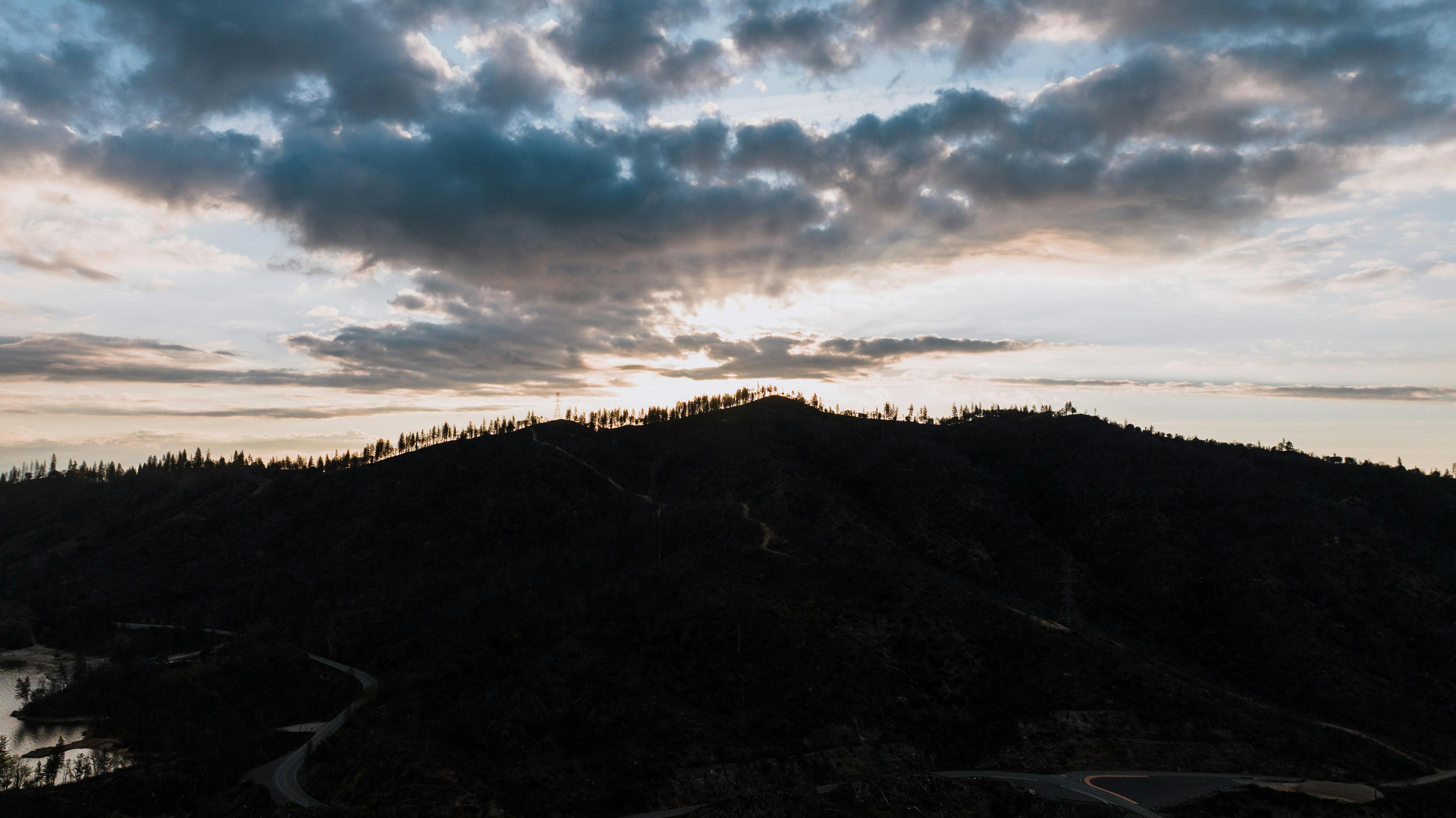 A sunset over a hill with clouds and trees · Free Stock Photo
