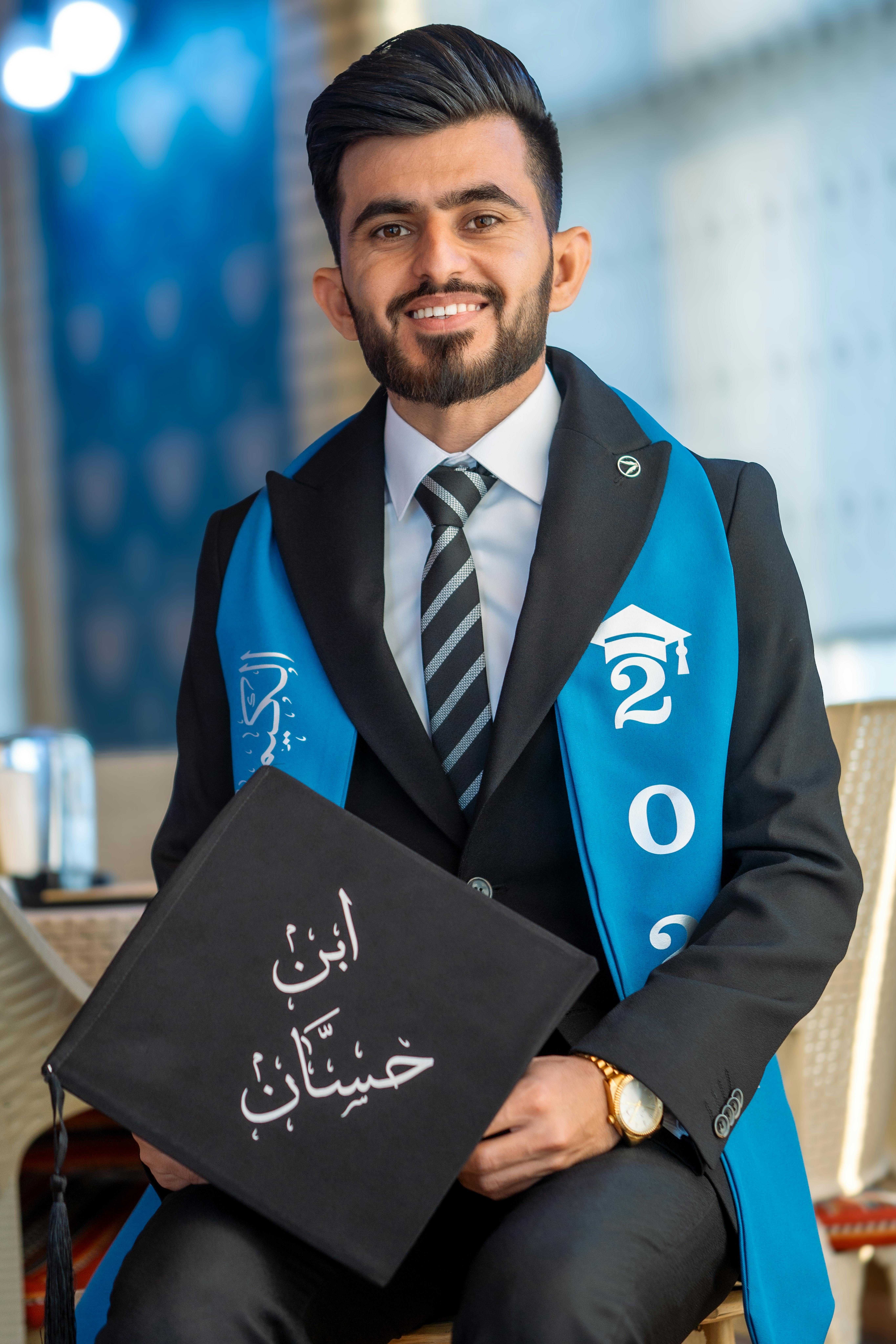 Smiling Graduate in Black Suit Holding Mortarboard · Free Stock Photo