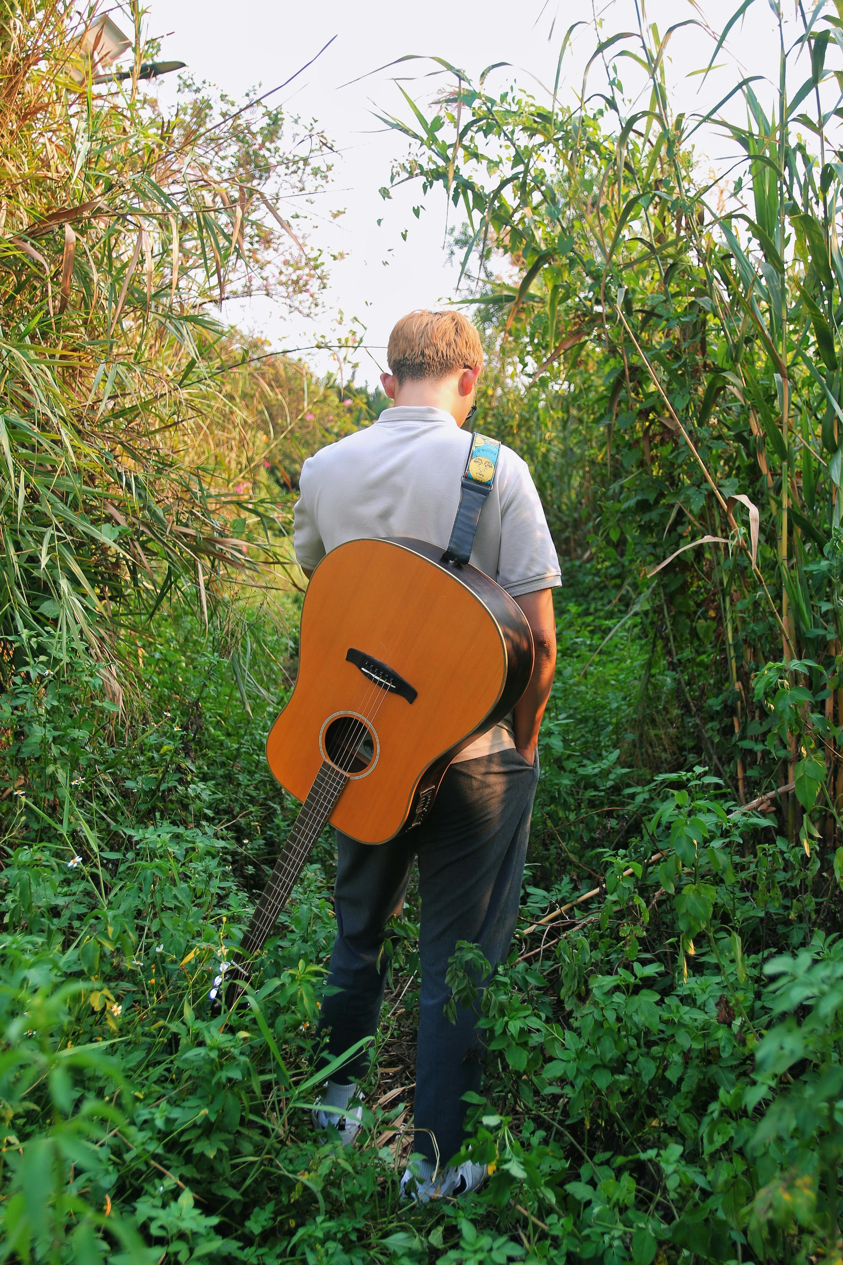 Back View of a Man with an Acoustic Guitar on His Back Standing among ...