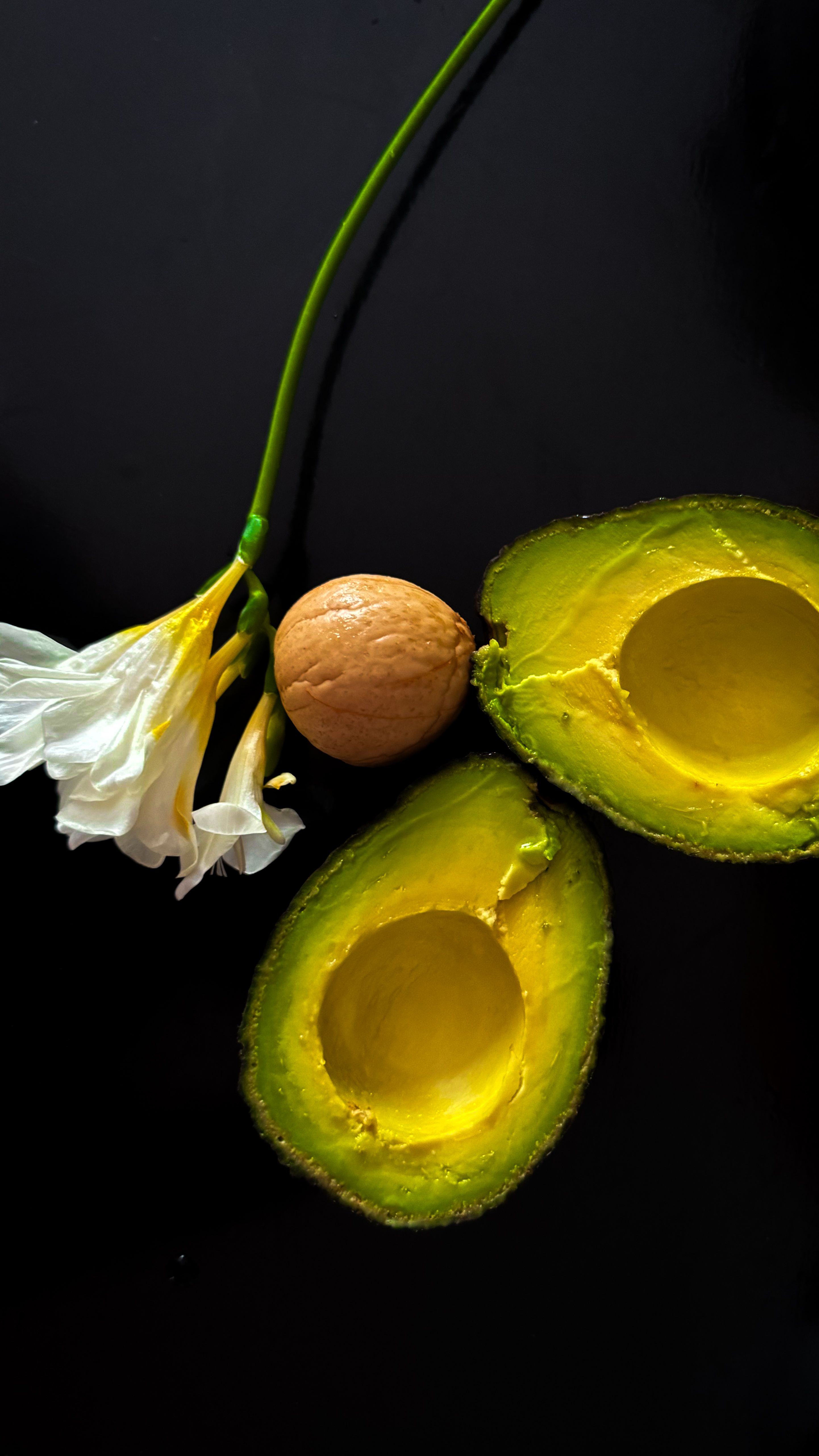 Top View of a Cut in Half Avocado and a Flower Lying on Black ...