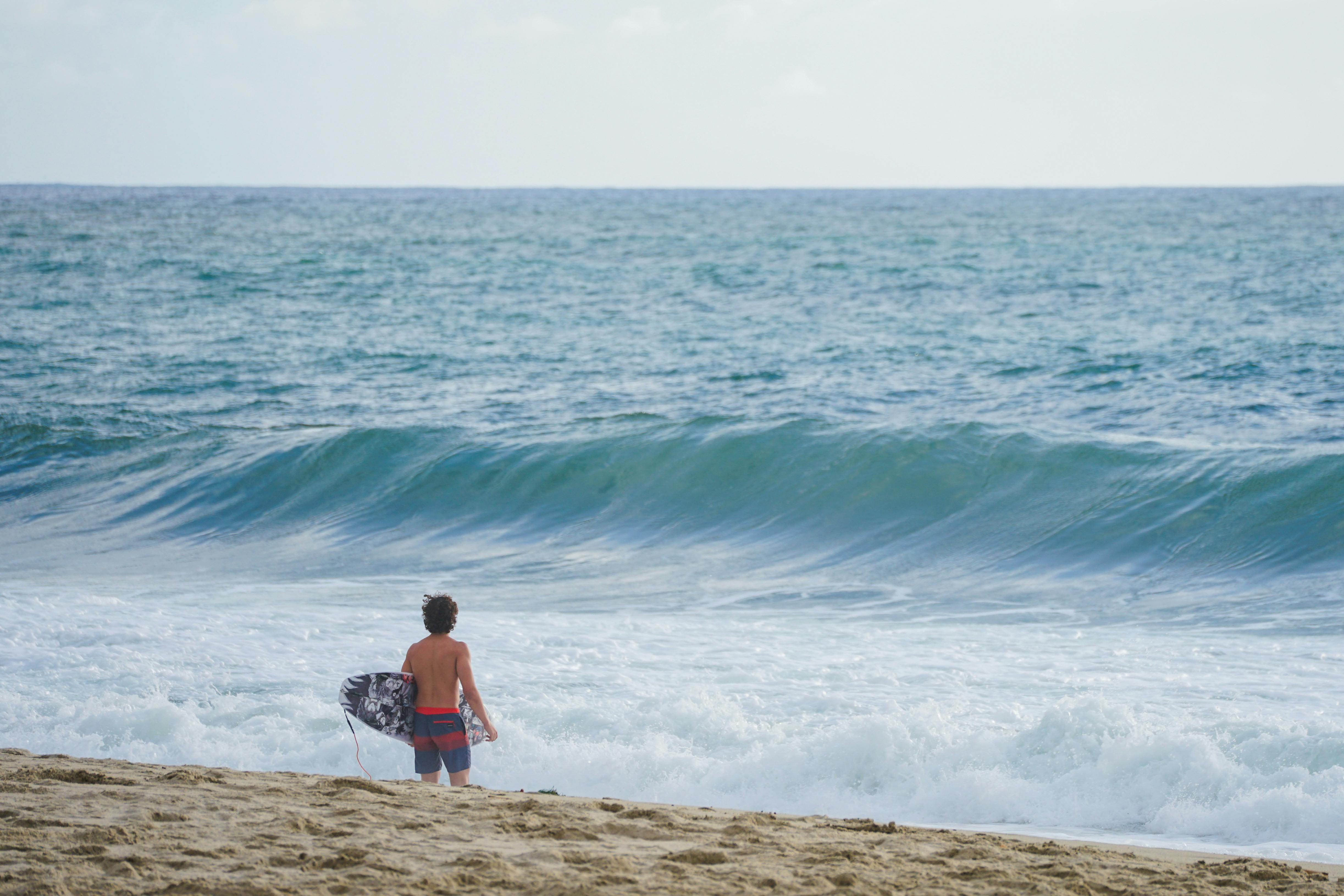 Tourist with Surfboard Looking at Waves from the Beach · Free Stock Photo