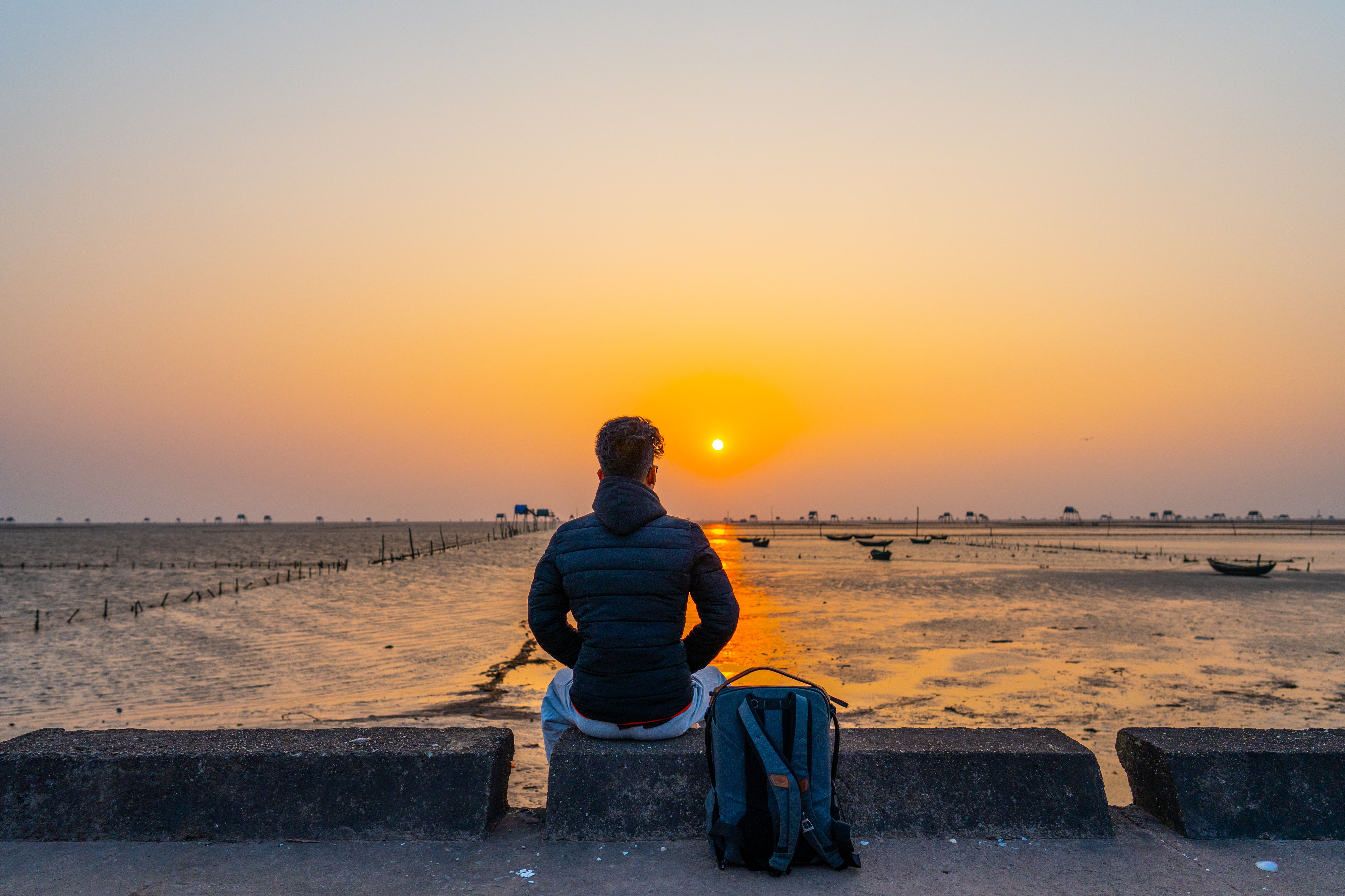 Back View of Man in Jacket Sitting on Sea Shore at Sunset · Free Stock ...