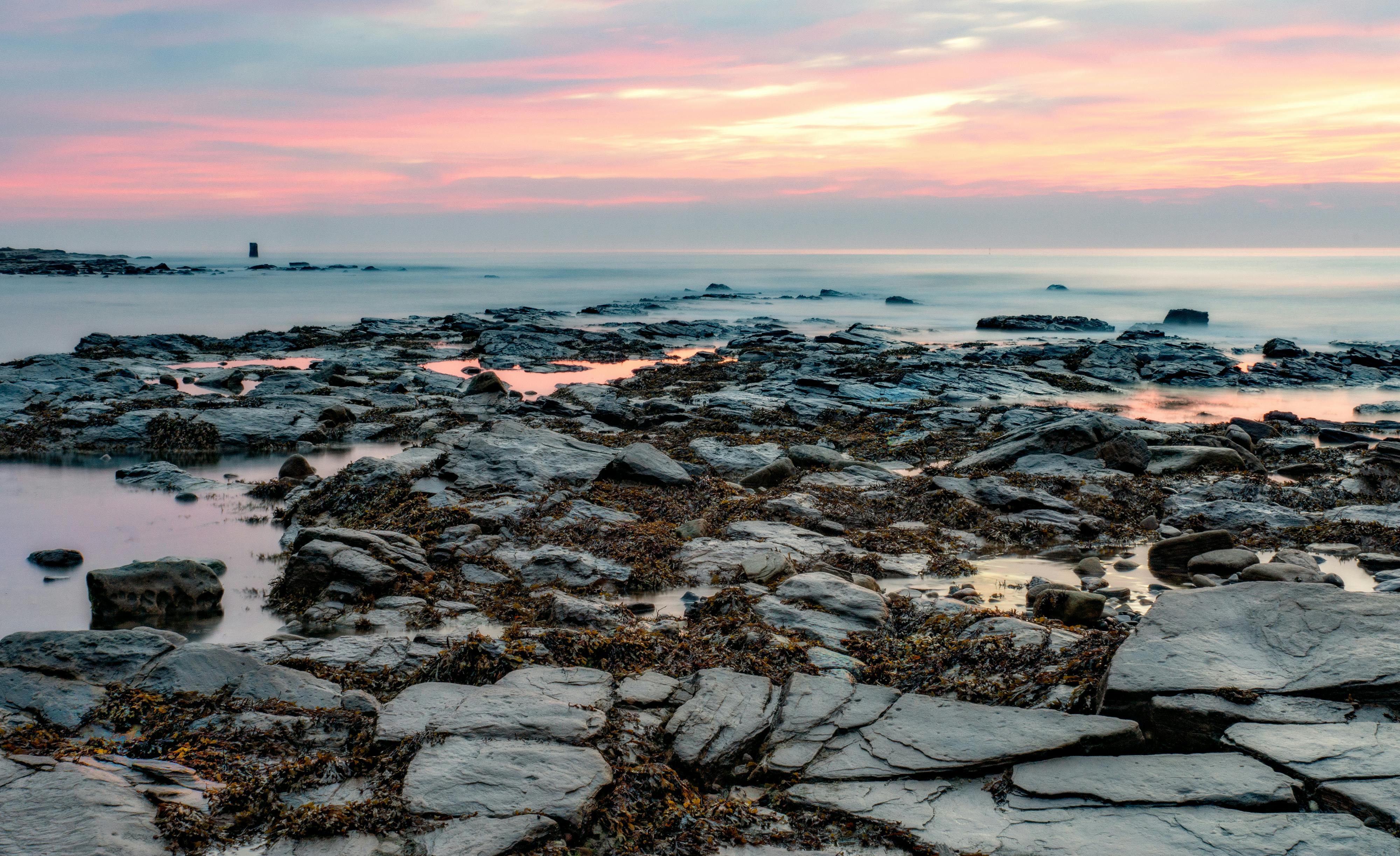 A sunset over rocky shoreline with rocks and water · Free Stock Photo