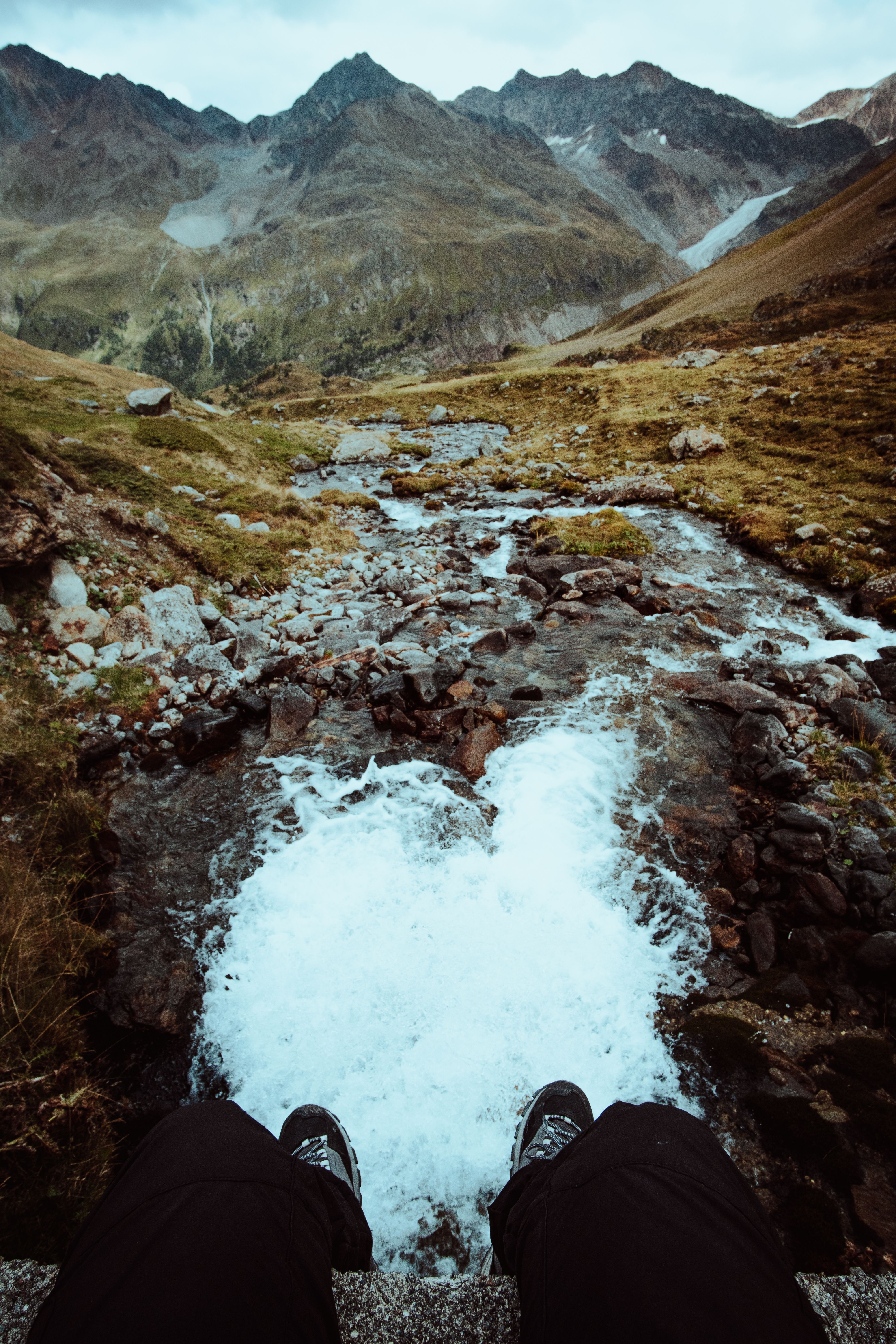A person sitting on a rock in front of a stream · Free Stock Photo